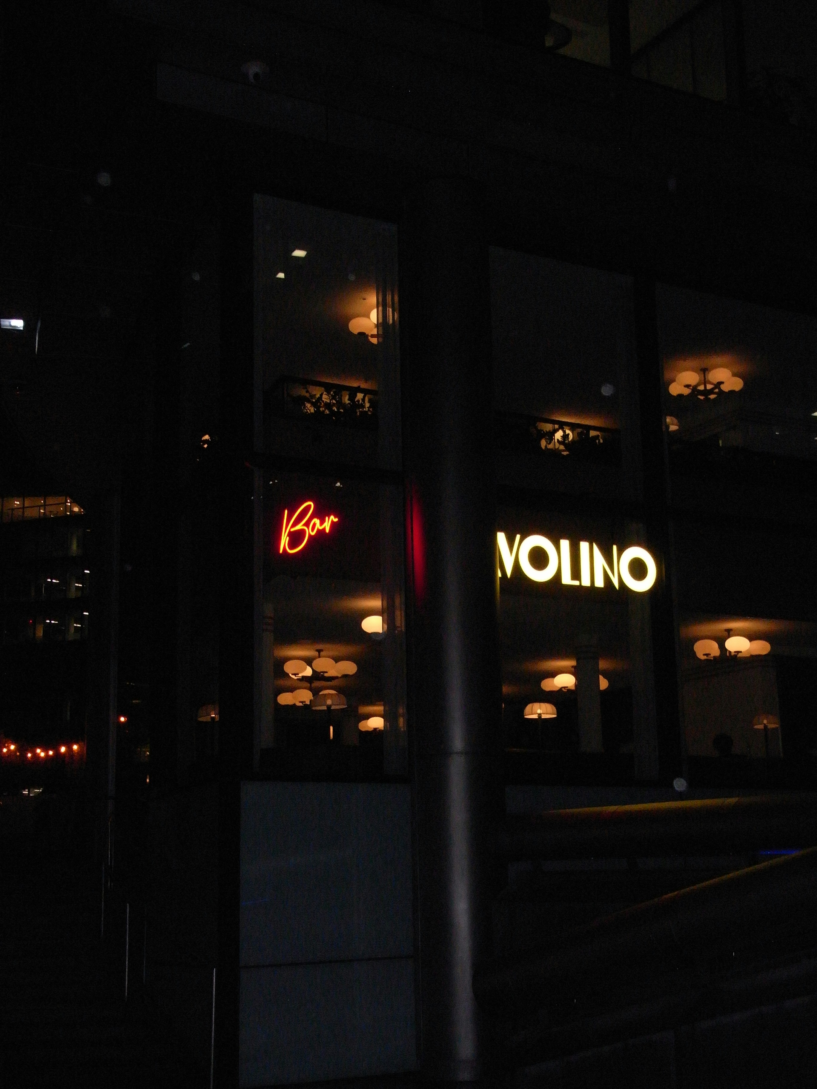 Neon sign of 'Volino' and 'Bar' glowing against a darkened urban backdrop, highlighting the inviting ambiance of the venue.
