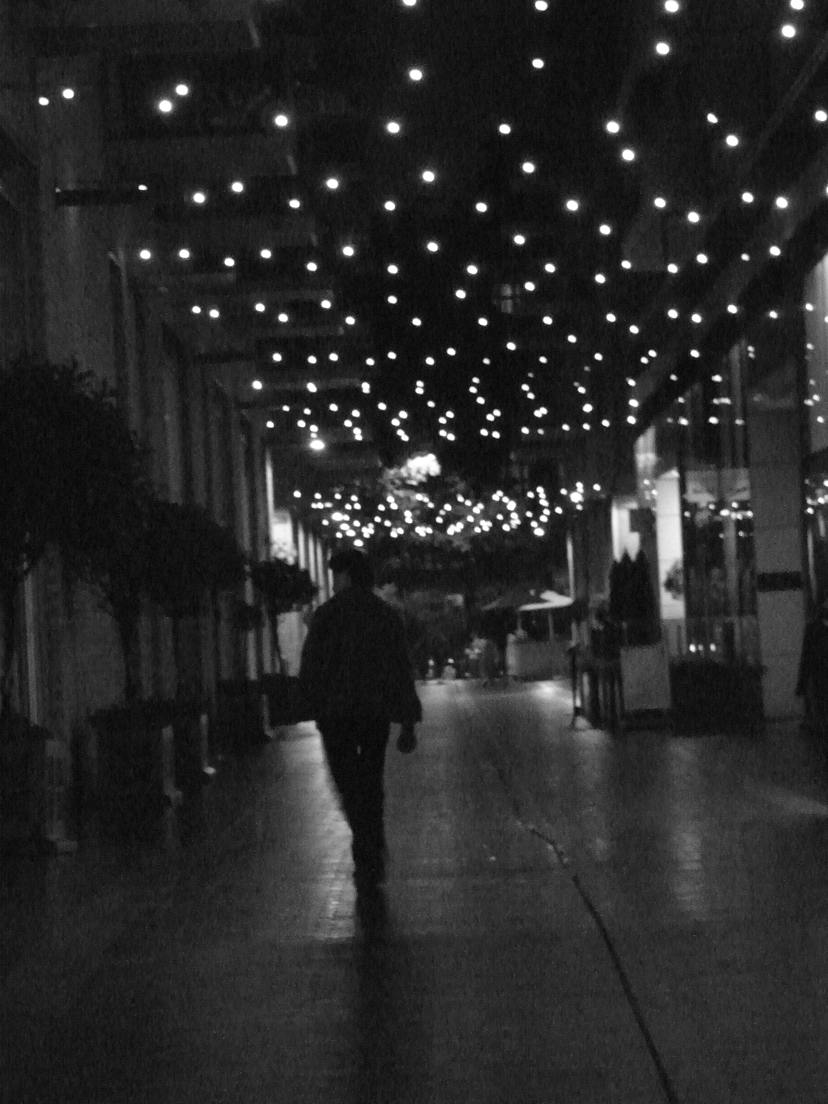 Silhouette of a lone figure walking down a dimly lit corridor adorned with sparkling lights. The scene captures a serene evening atmosphere.