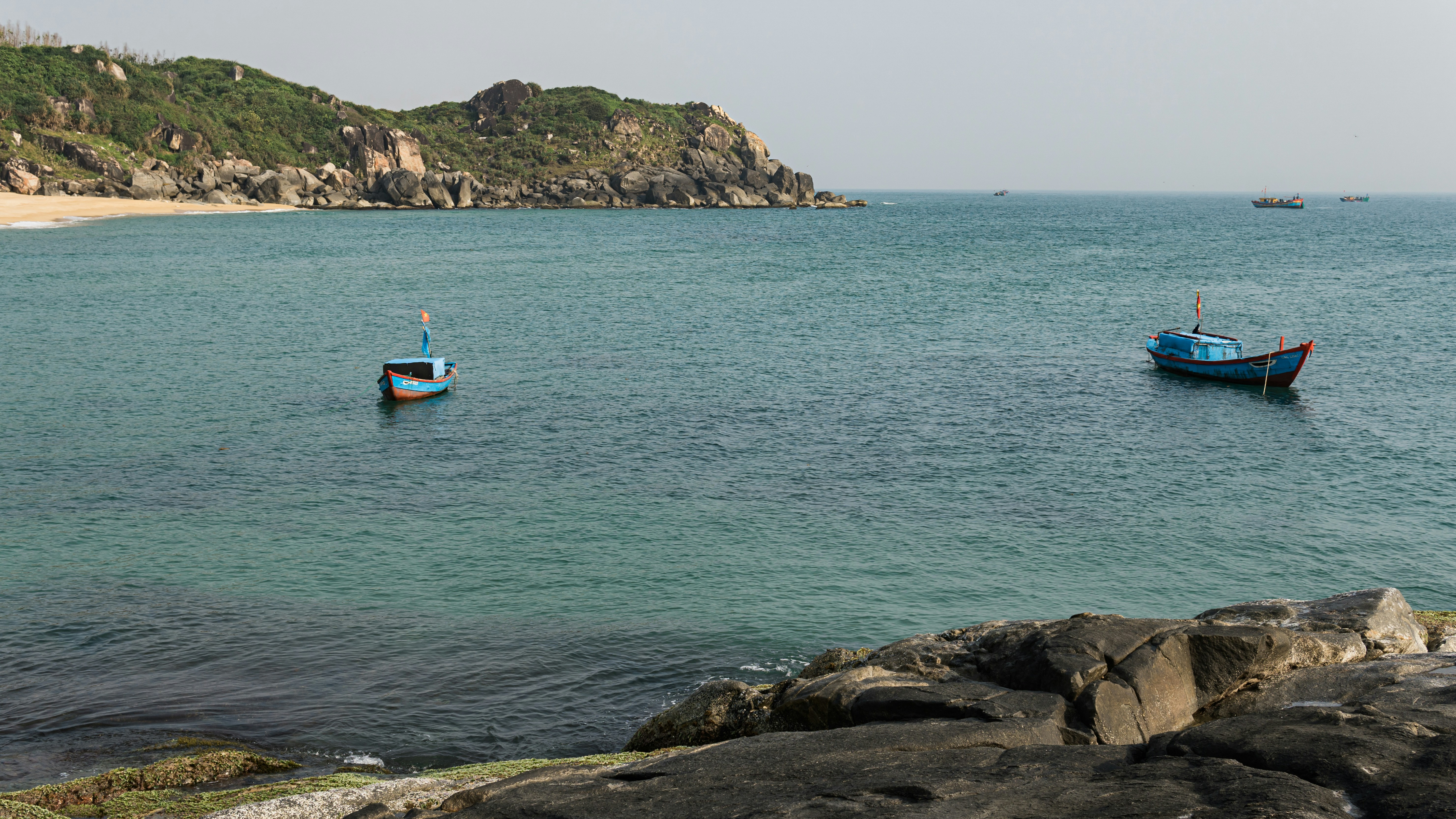 Two fishing boats gently bobbing in the calm waters of a secluded harbor, framed by rocky shores and lush greenery.