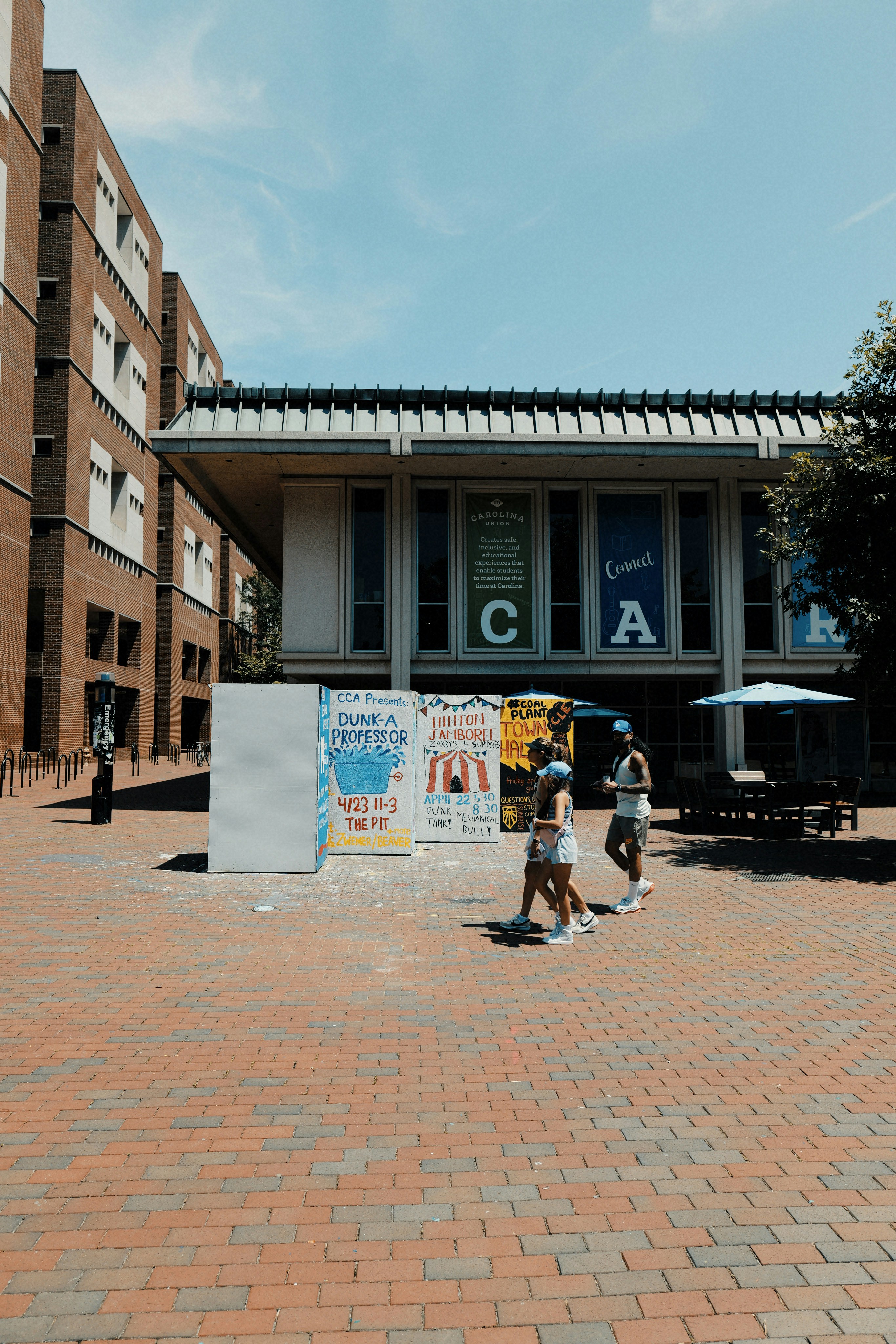 Students walk past posters on a sunny day.