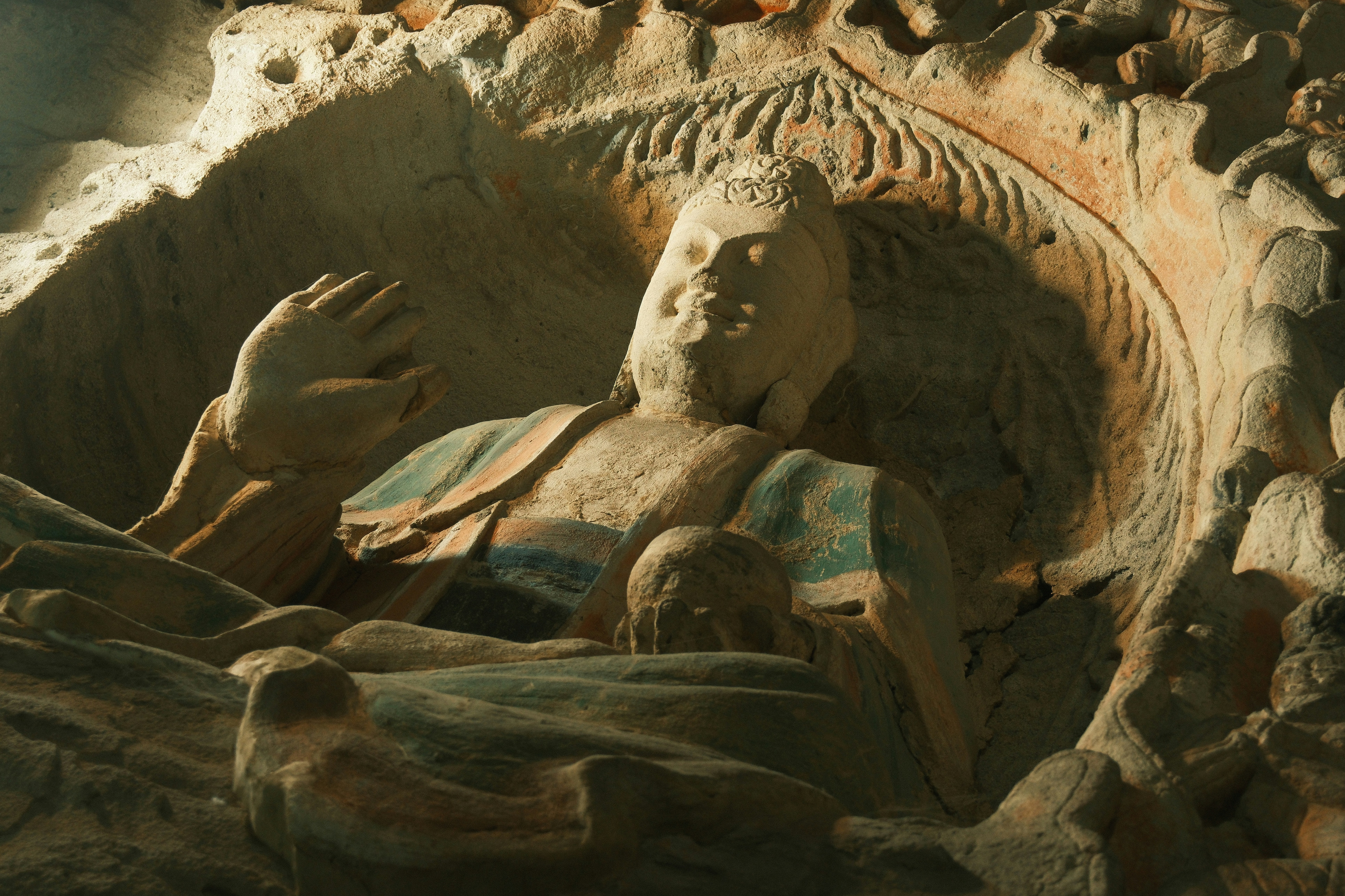 Intricate sculpture of a seated Buddha with an outstretched hand, set against a textured rock background. The piece reflects ancient artistry and spiritual significance.
