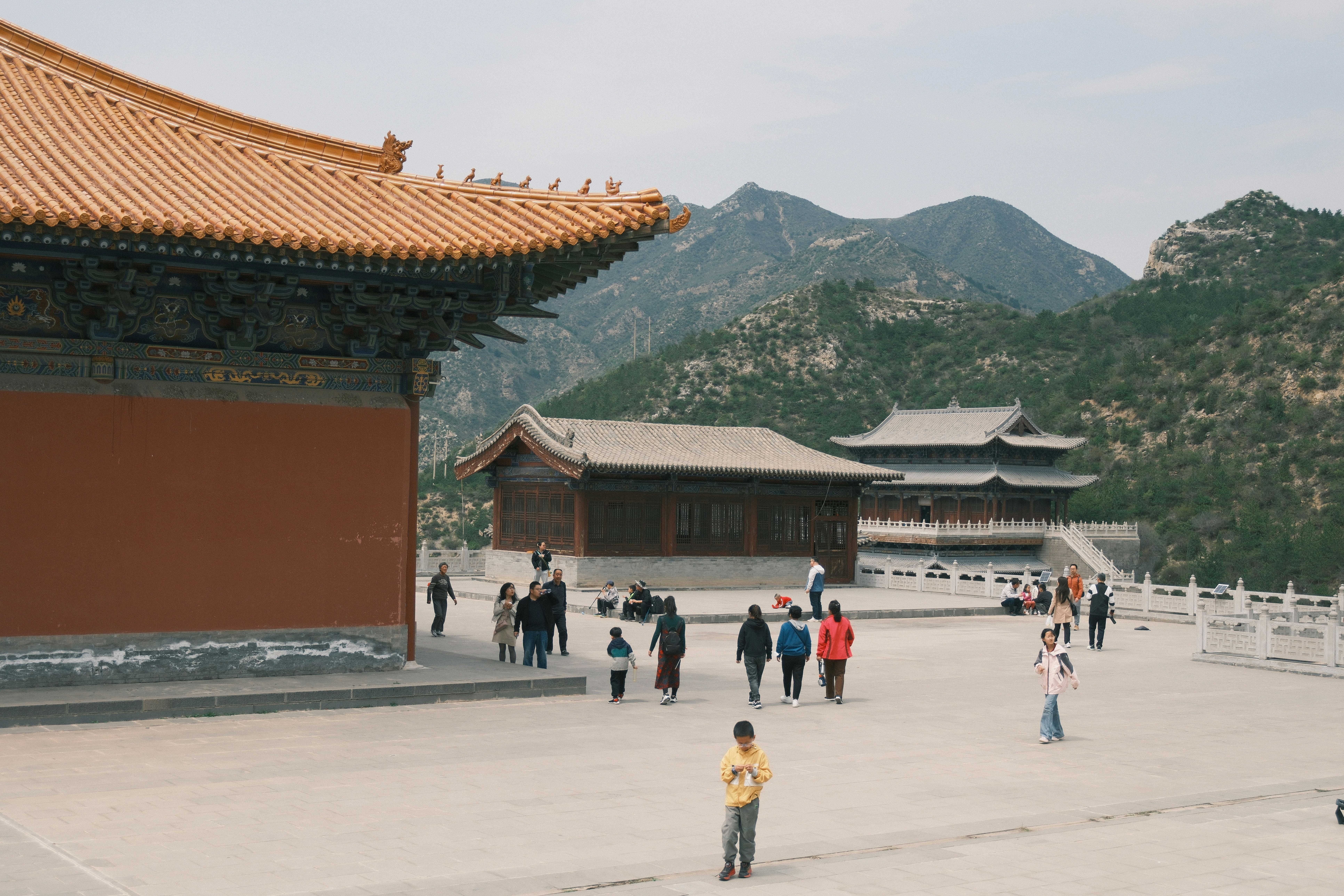 Visitors exploring ancient architecture against a backdrop of majestic mountains. The scene captures a blend of cultural history and natural beauty.