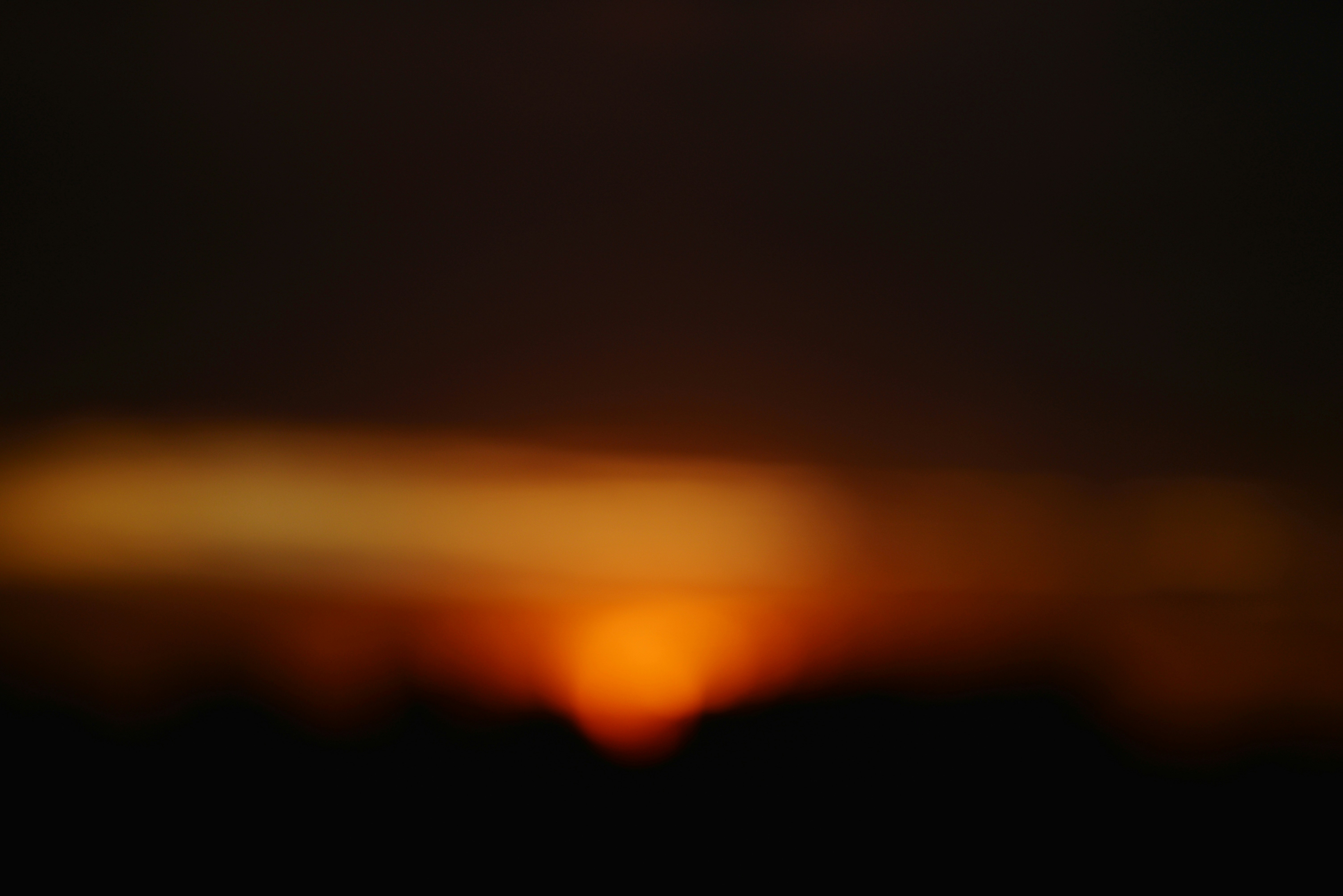 A blurred sunset scene featuring warm hues blending into a darkening sky, evoking a sense of tranquility and transition.