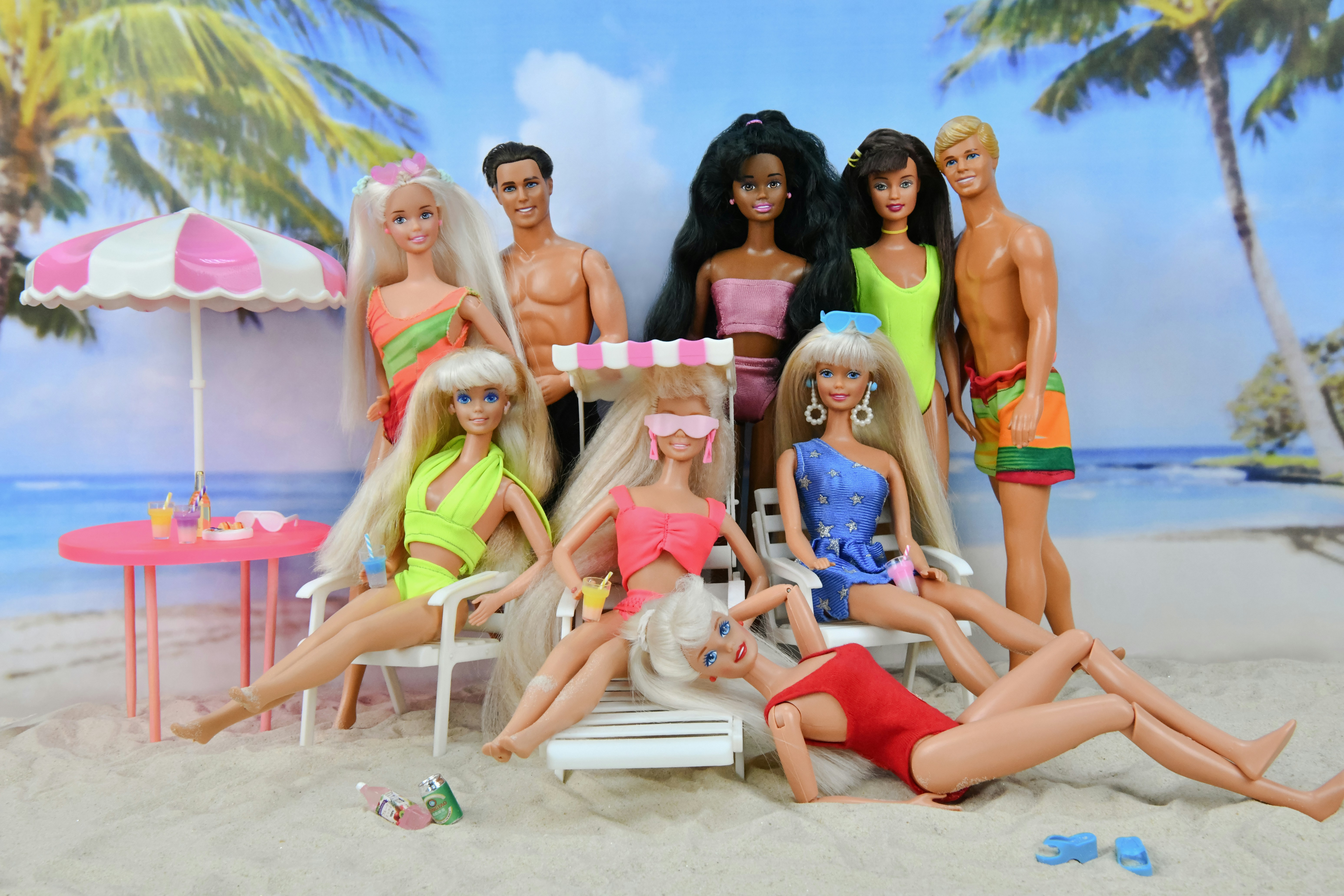 A lively assembly of Barbie dolls enjoying a beach day, complete with colorful swimwear and lounging chairs under a vibrant umbrella. The backdrop features a tropical paradise.