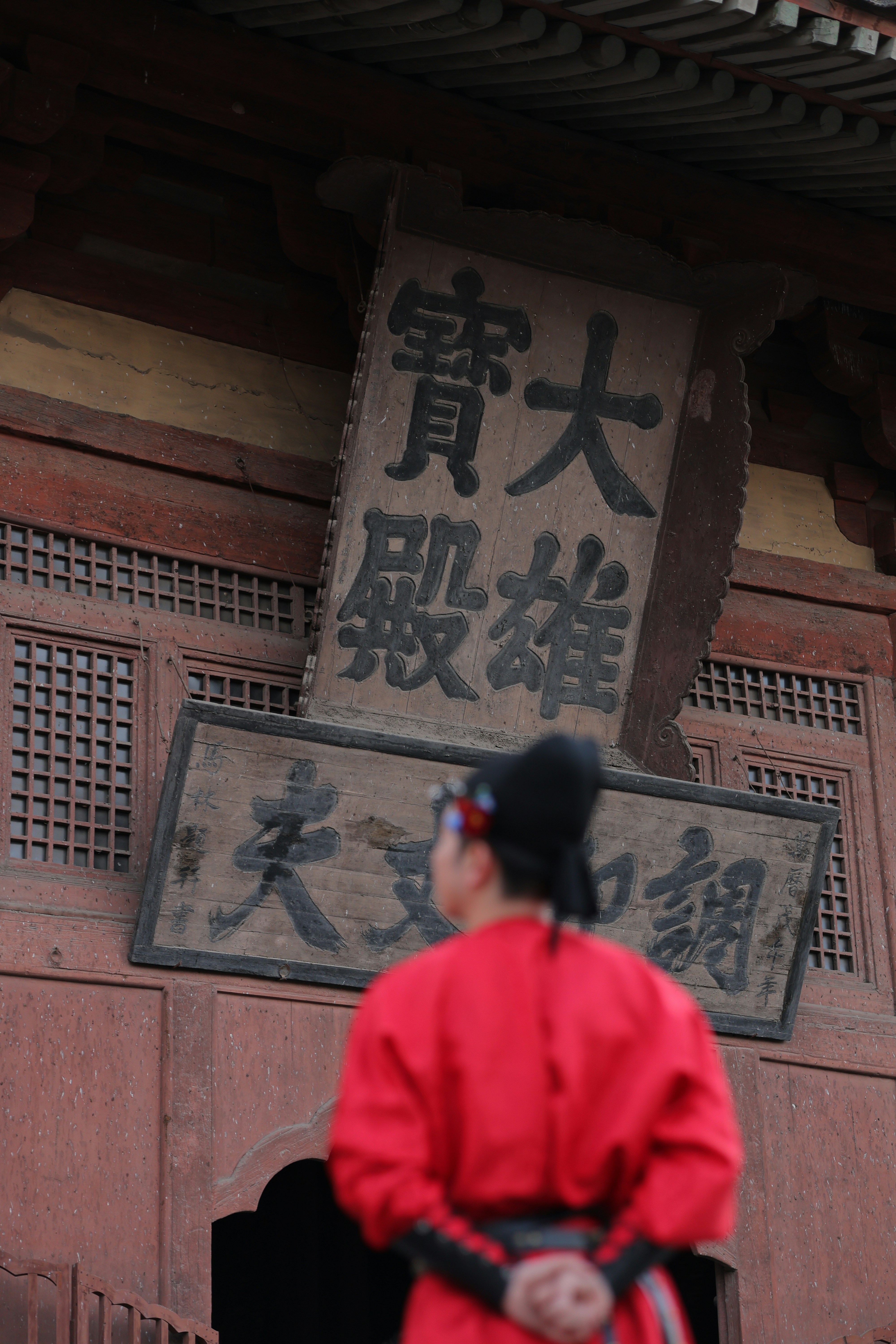 Crimson-clad silhouette before weathered temple signage