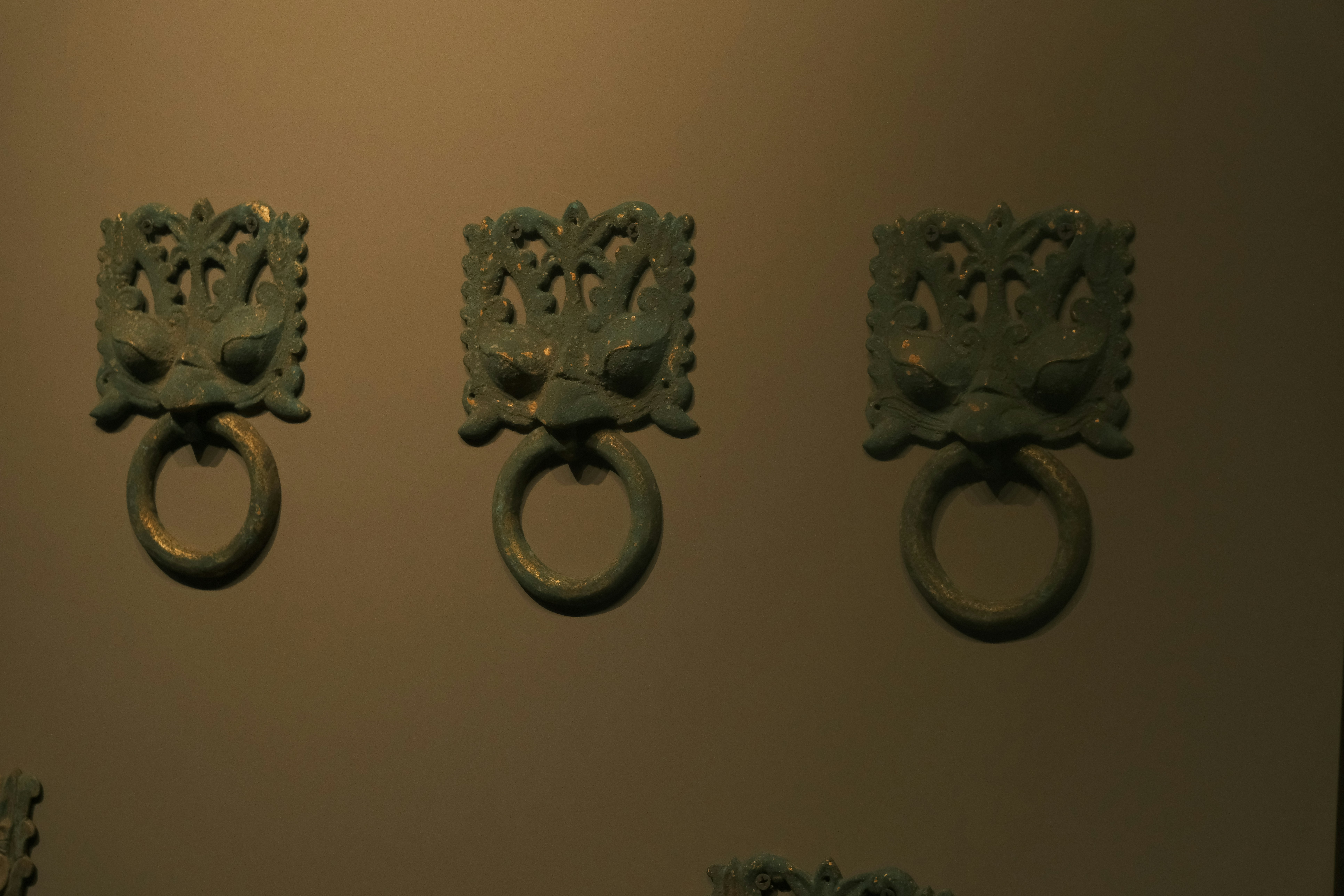 Three ornate bronze door knockers mounted on a muted wall, showcasing intricate craftsmanship and historical significance.
