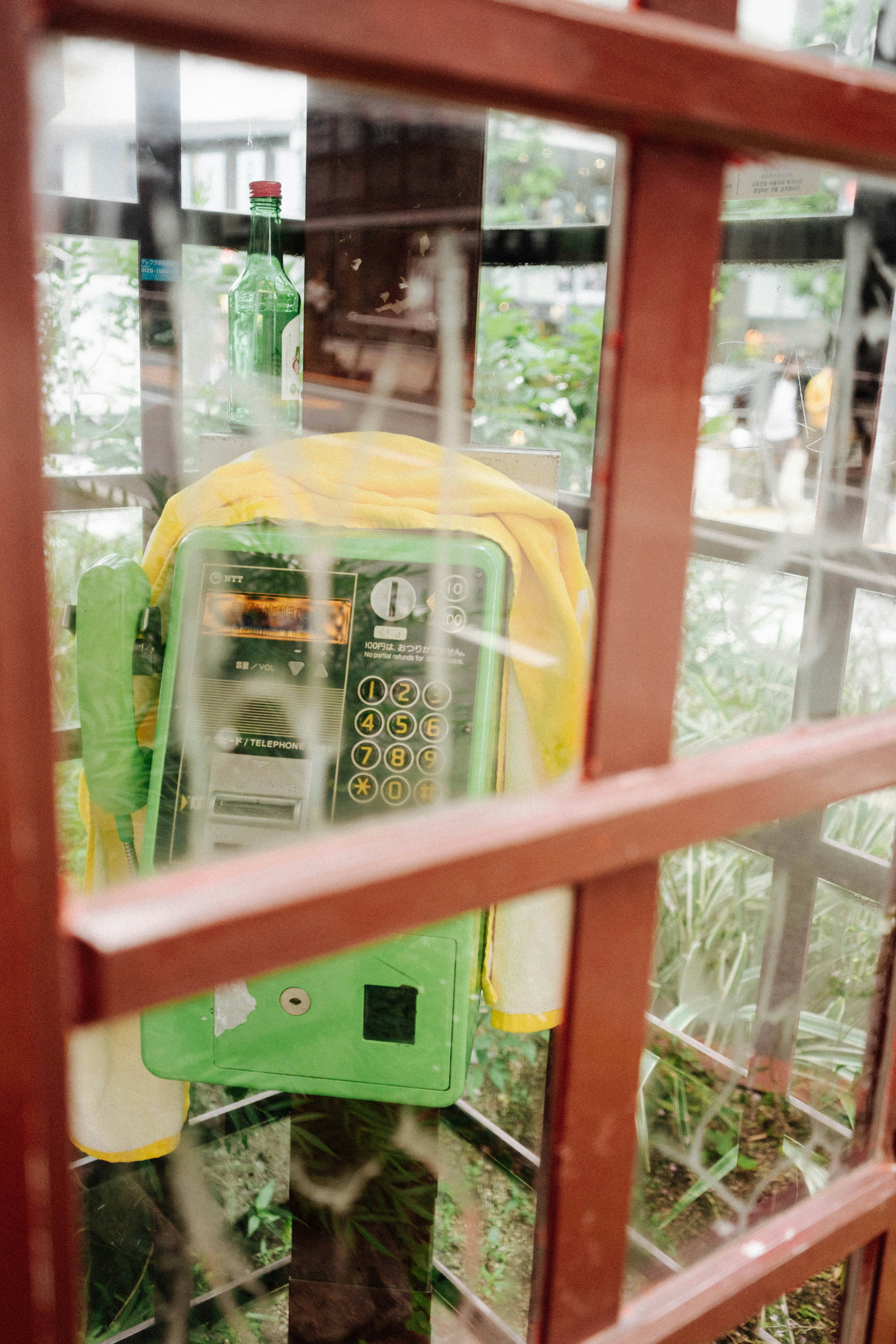 Green payphone inside a red-barred booth with yellow cloth.