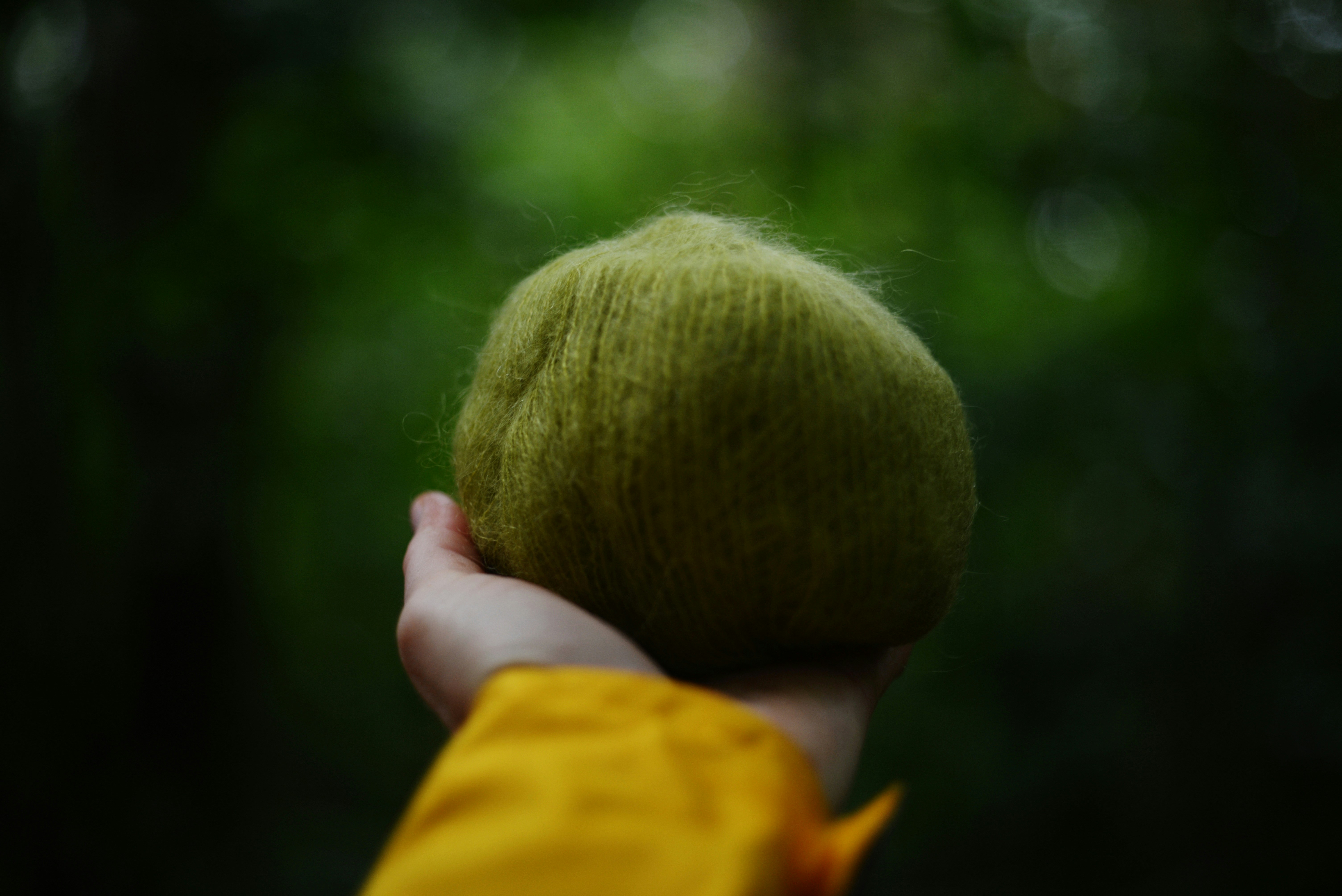 Hand holding a fuzzy green object outdoors.