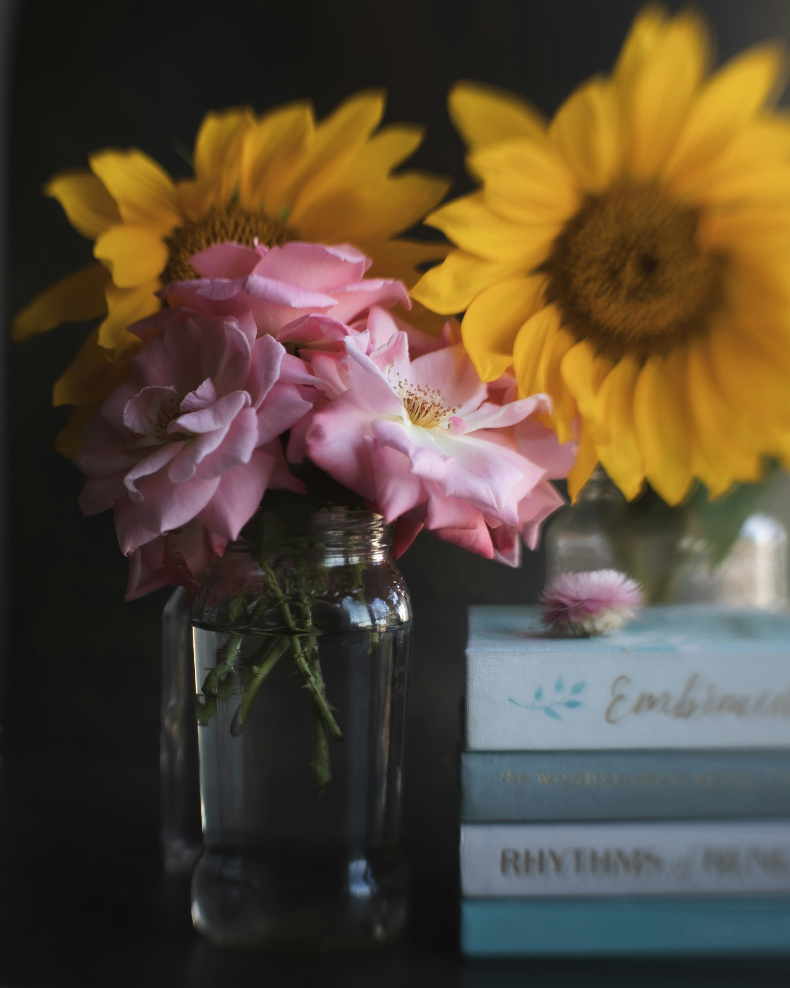 Sunflowers and pink roses in a jar beside books.