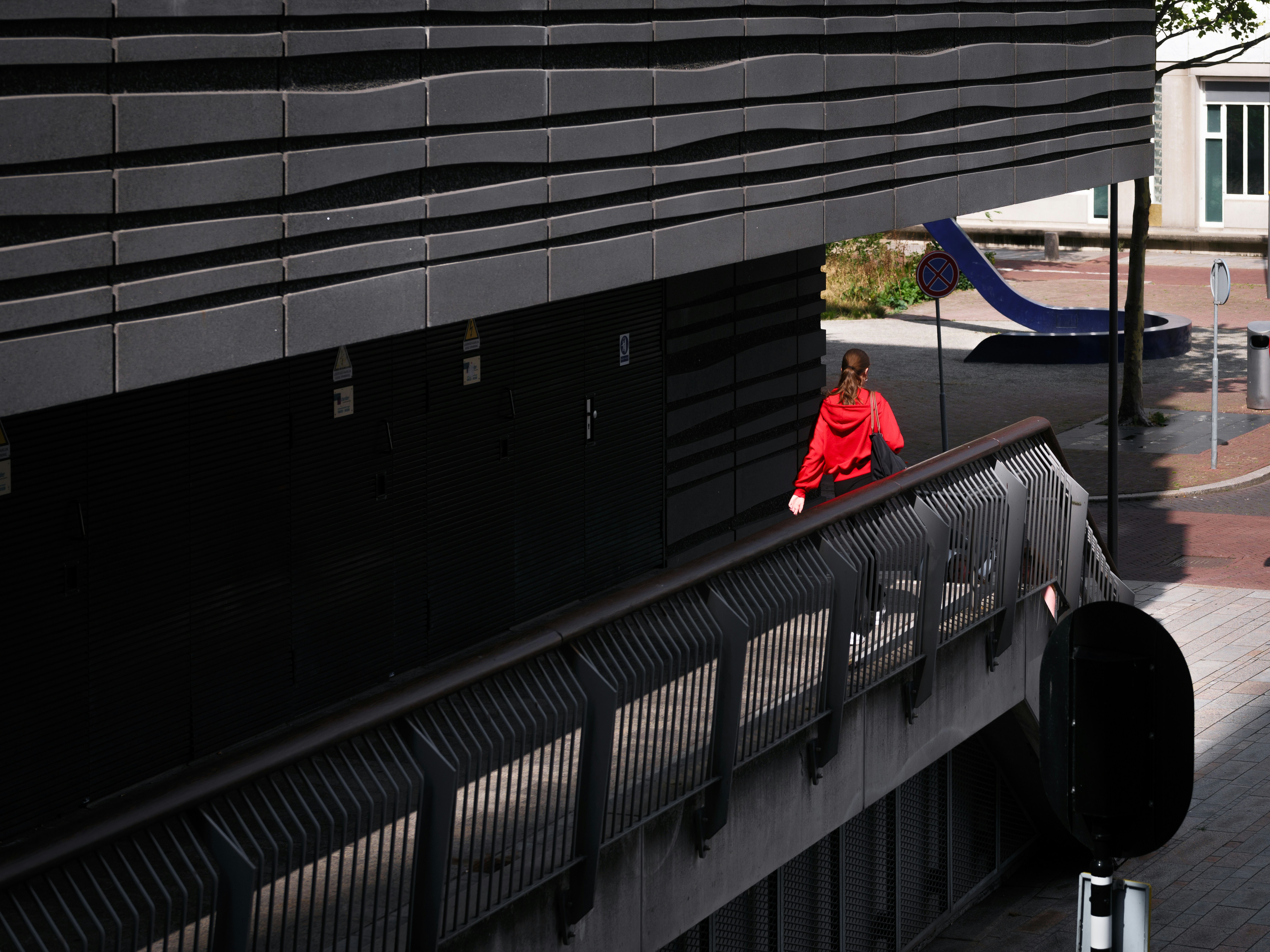 Pedestrian on a sunlit elevated walkway beside a dark modern facade