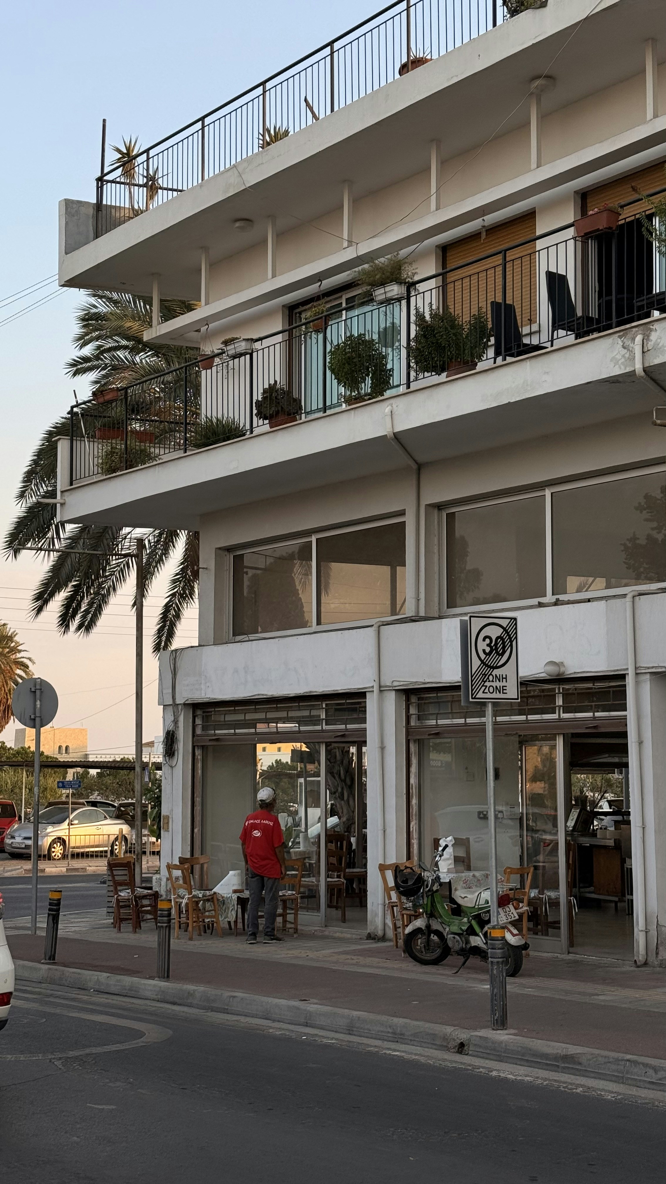 Red Shirt at the Sunlit Café: Balconies and Plants in an Urban Streetfront