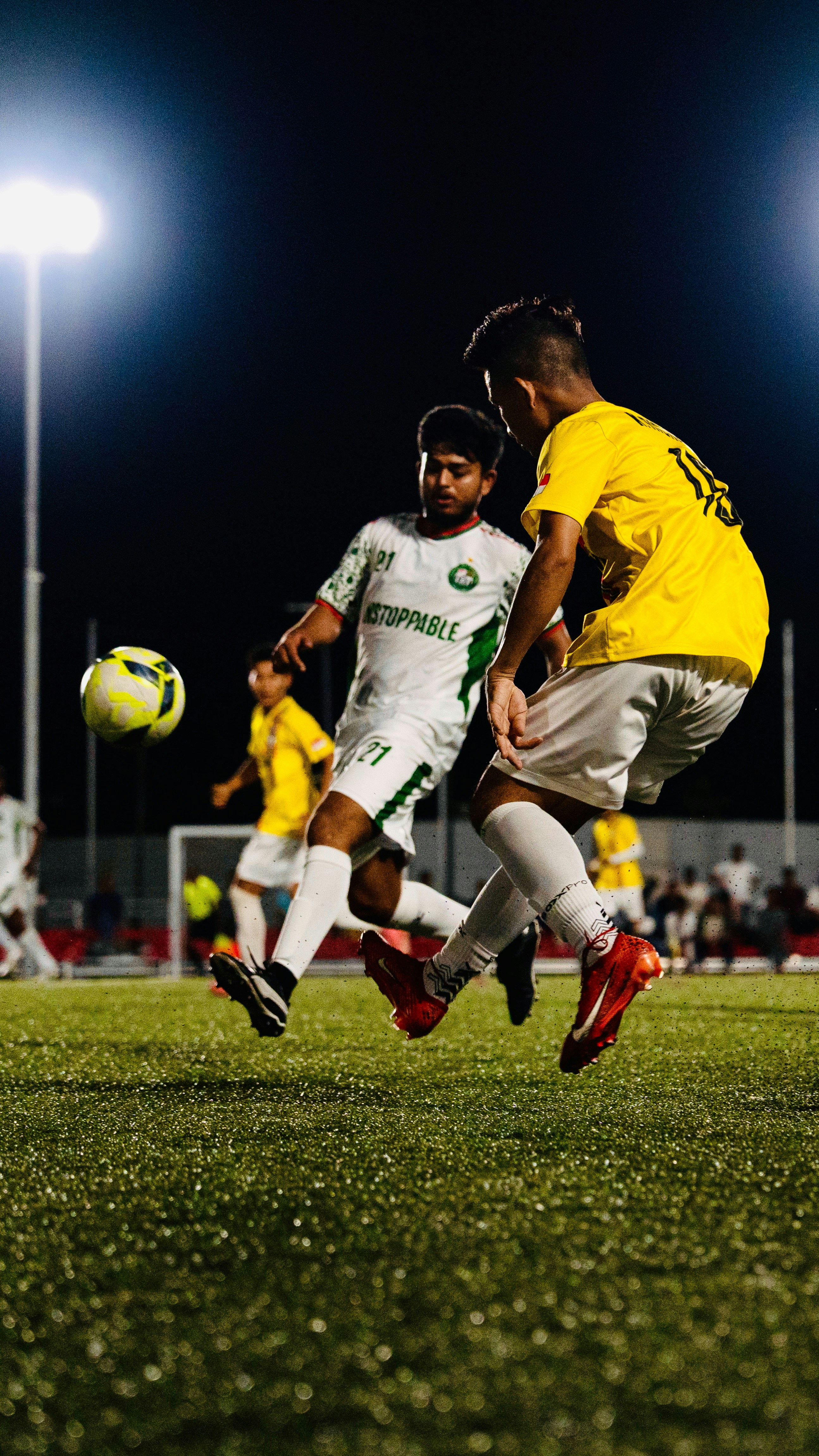Midair Challenge Under Night Floodlights: Yellow and White Duel for the Ball