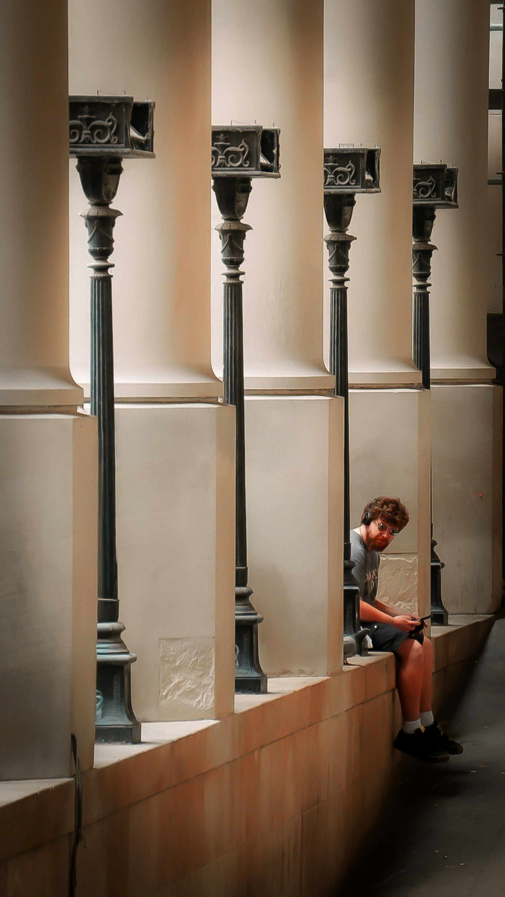 Quiet Pause Under Iron Columns: a solitary figure between ornate lampposts