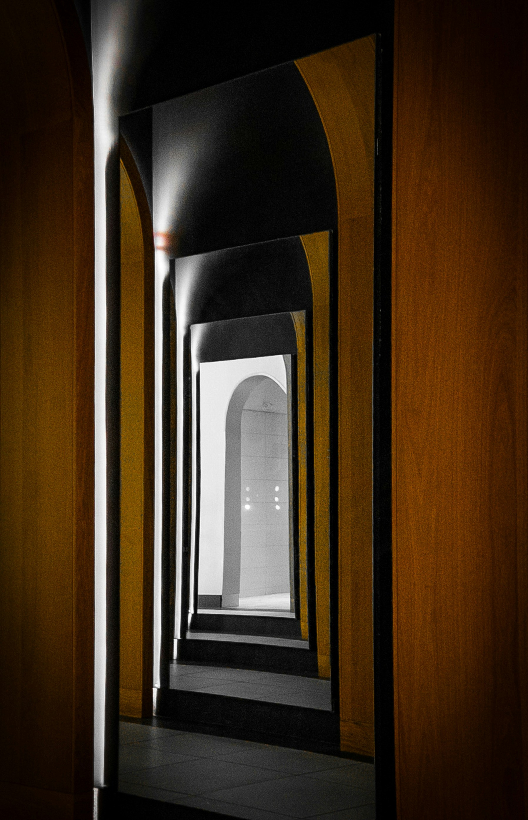 A series of reflective arches create a mesmerizing tunnel effect, showcasing contrasting textures and lighting. The interplay of dark and light elements draws the viewer deeper into the scene.