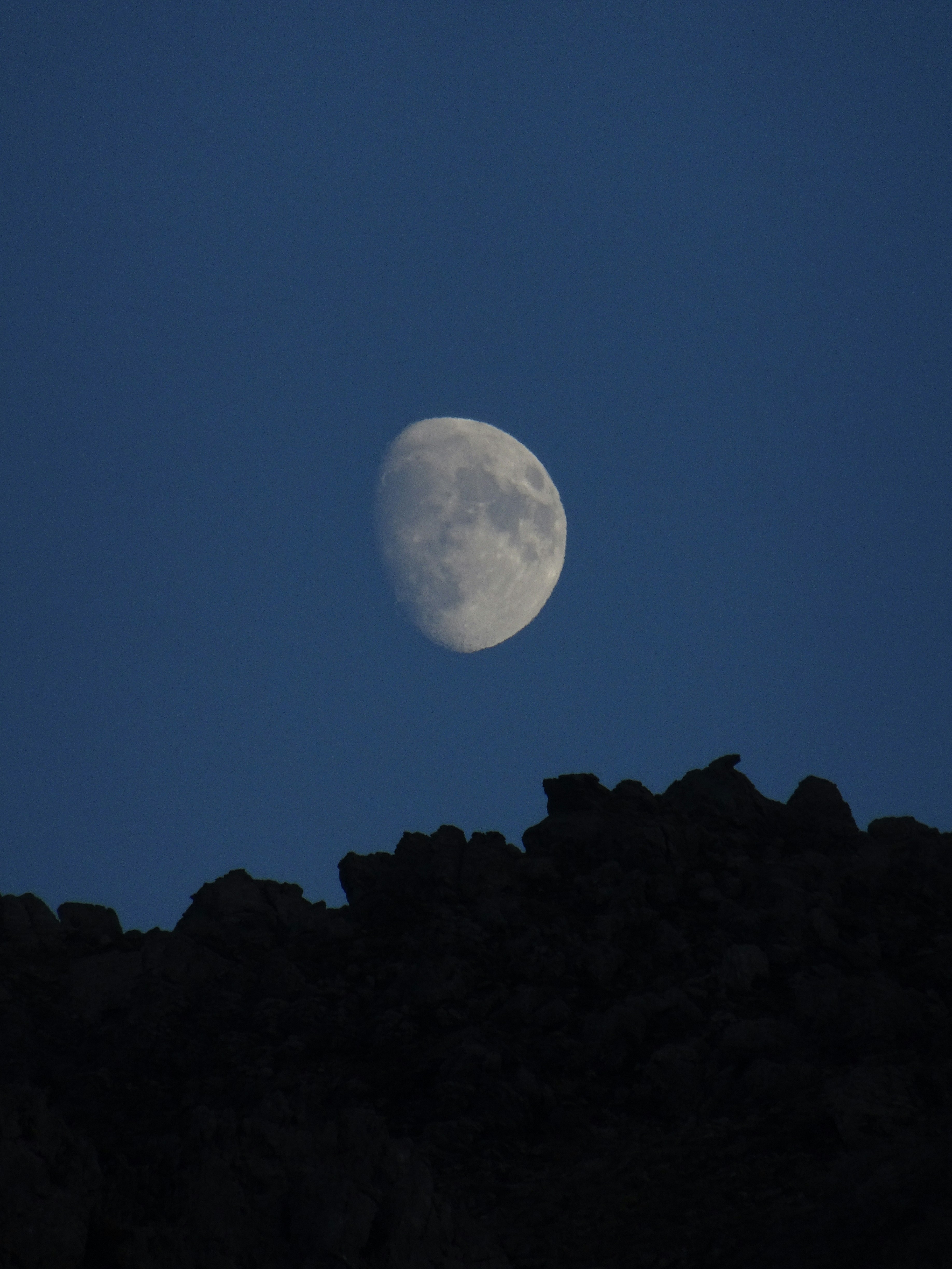 The moon hovers over a dark mountain ridge.
