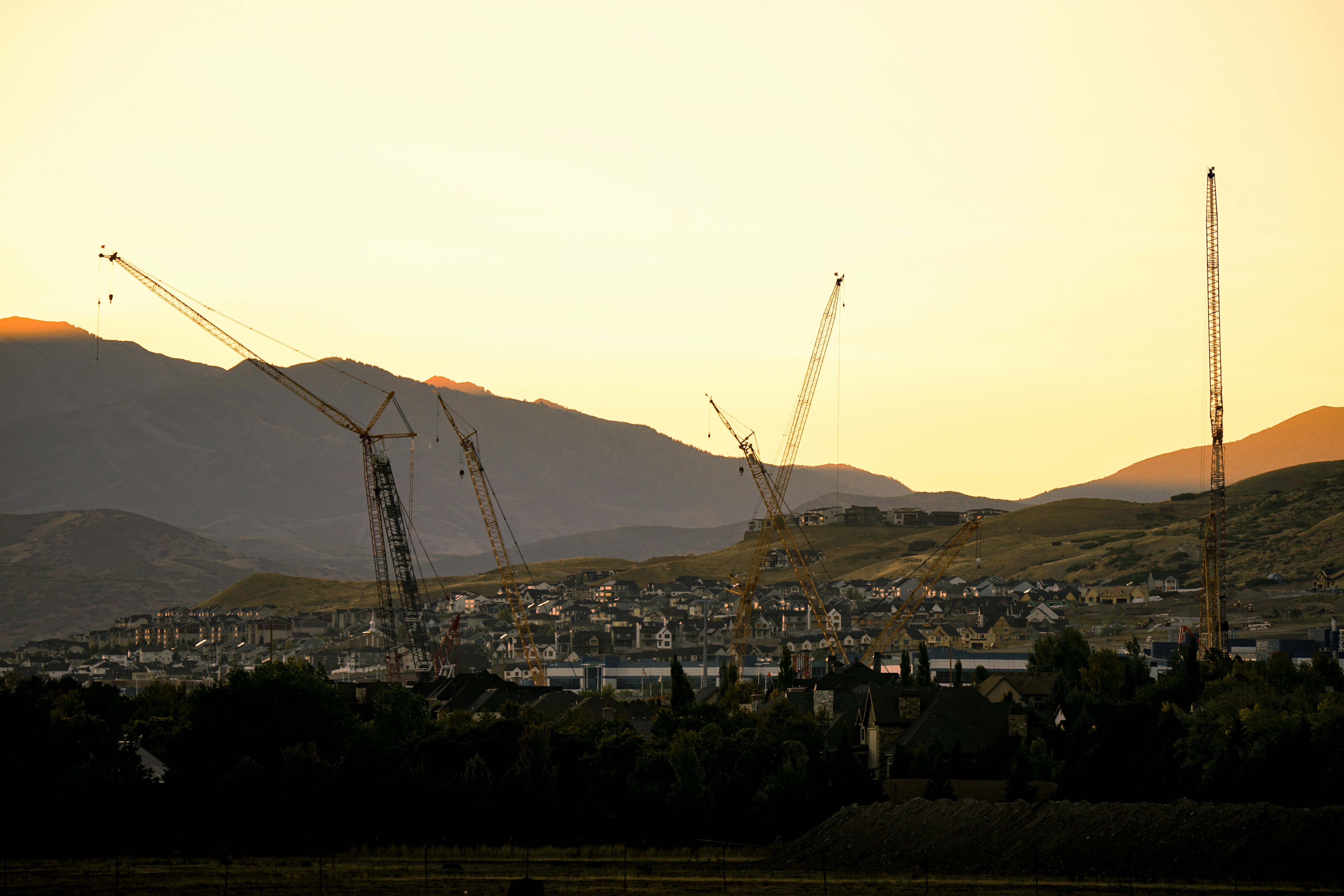 Construction on the expansion of the Texas Instruments chip manufacturing facility in Lehi, Utah | Construction cranes rise against a hazy mountain sunset.