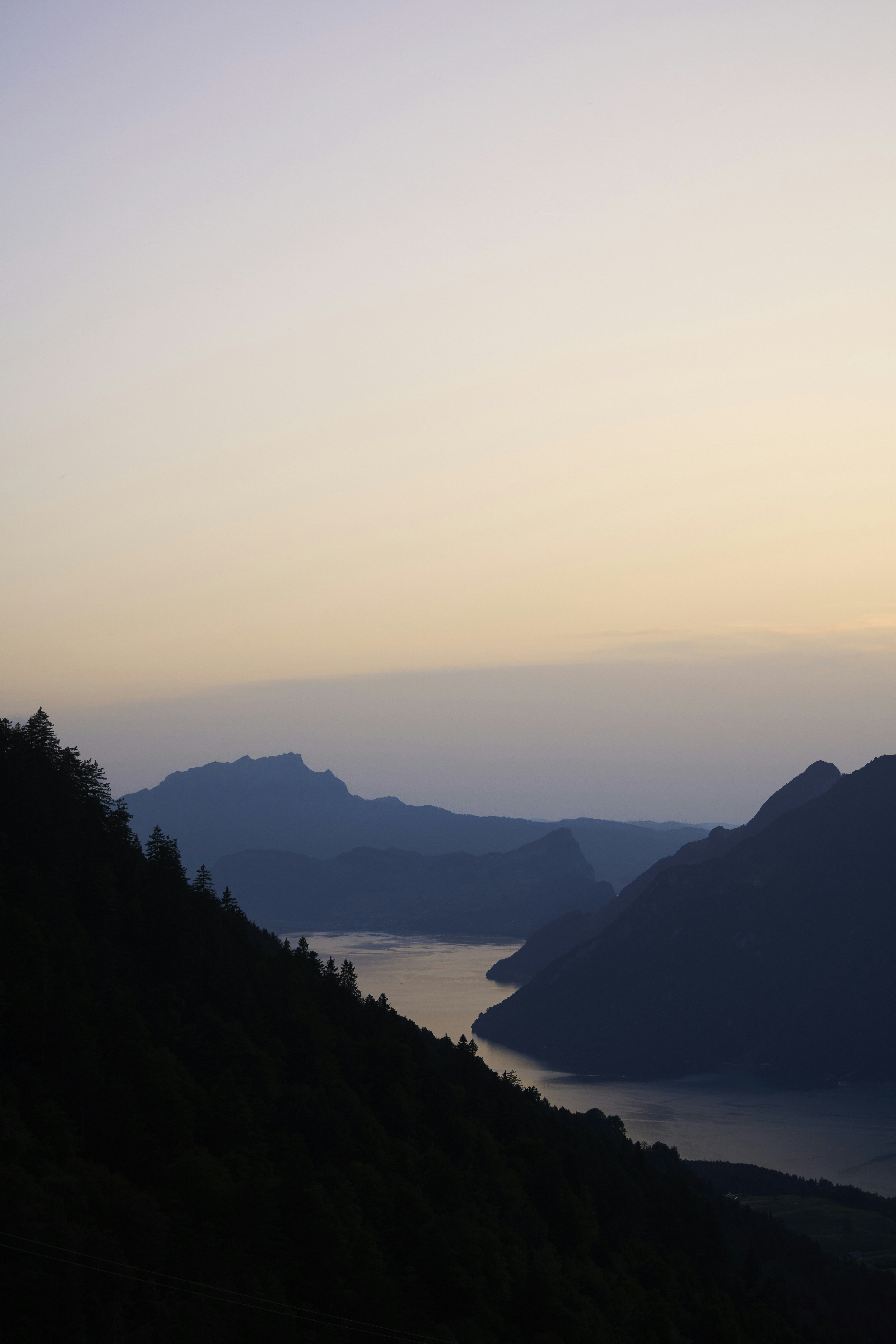 Soft hues of twilight illuminate distant mountain ranges and a serene lake, creating a tranquil landscape. The scene captures the transition from day to night.