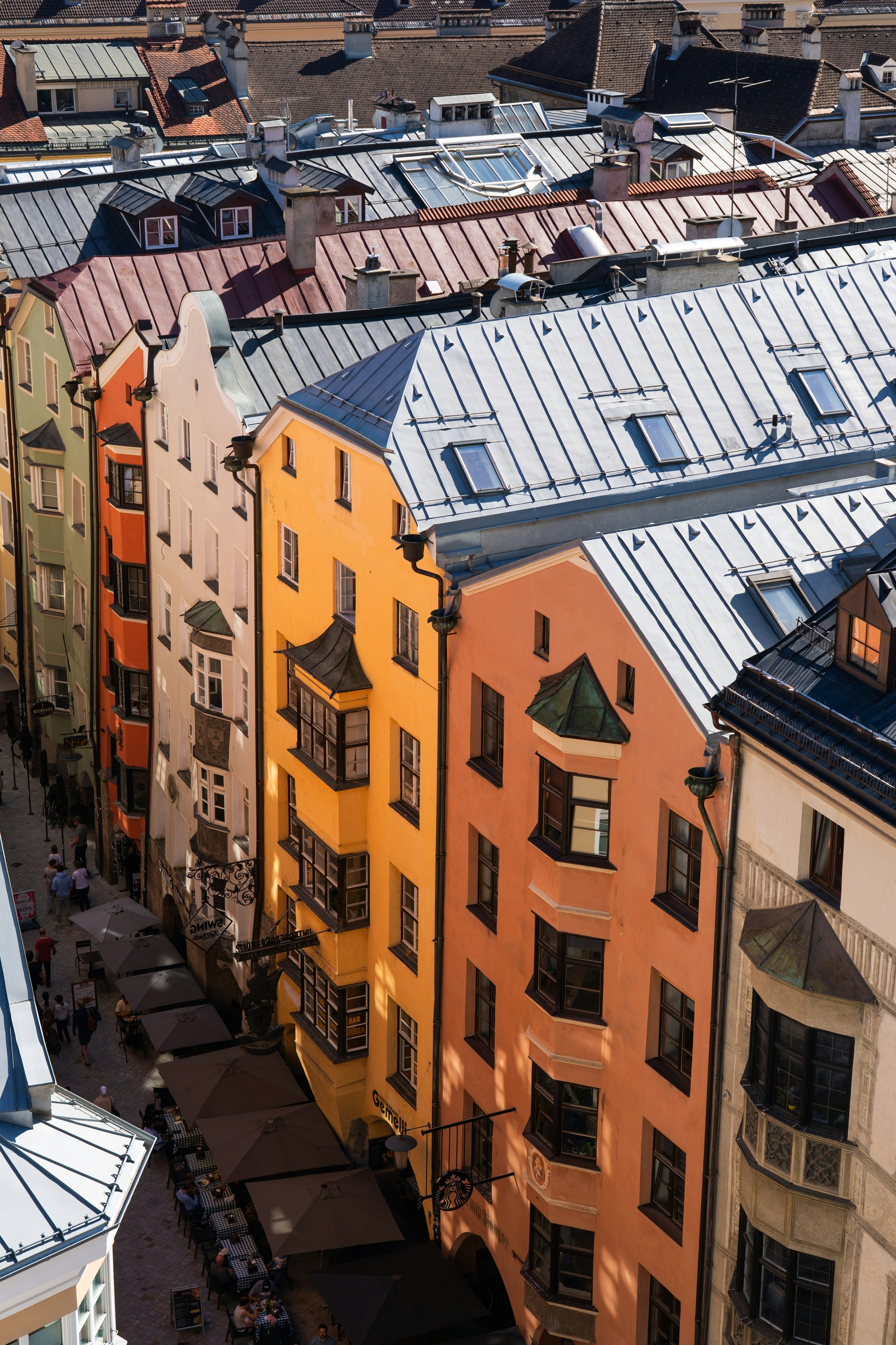 Vibrant facades of historic buildings line a narrow street, showcasing a blend of architectural styles and hues. Outdoor seating adds a lively touch to the urban scene.