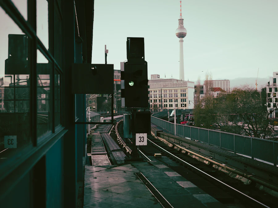 Elevated train tracks leading toward a green signal light with a distant TV tower and city buildings under a pale sky.