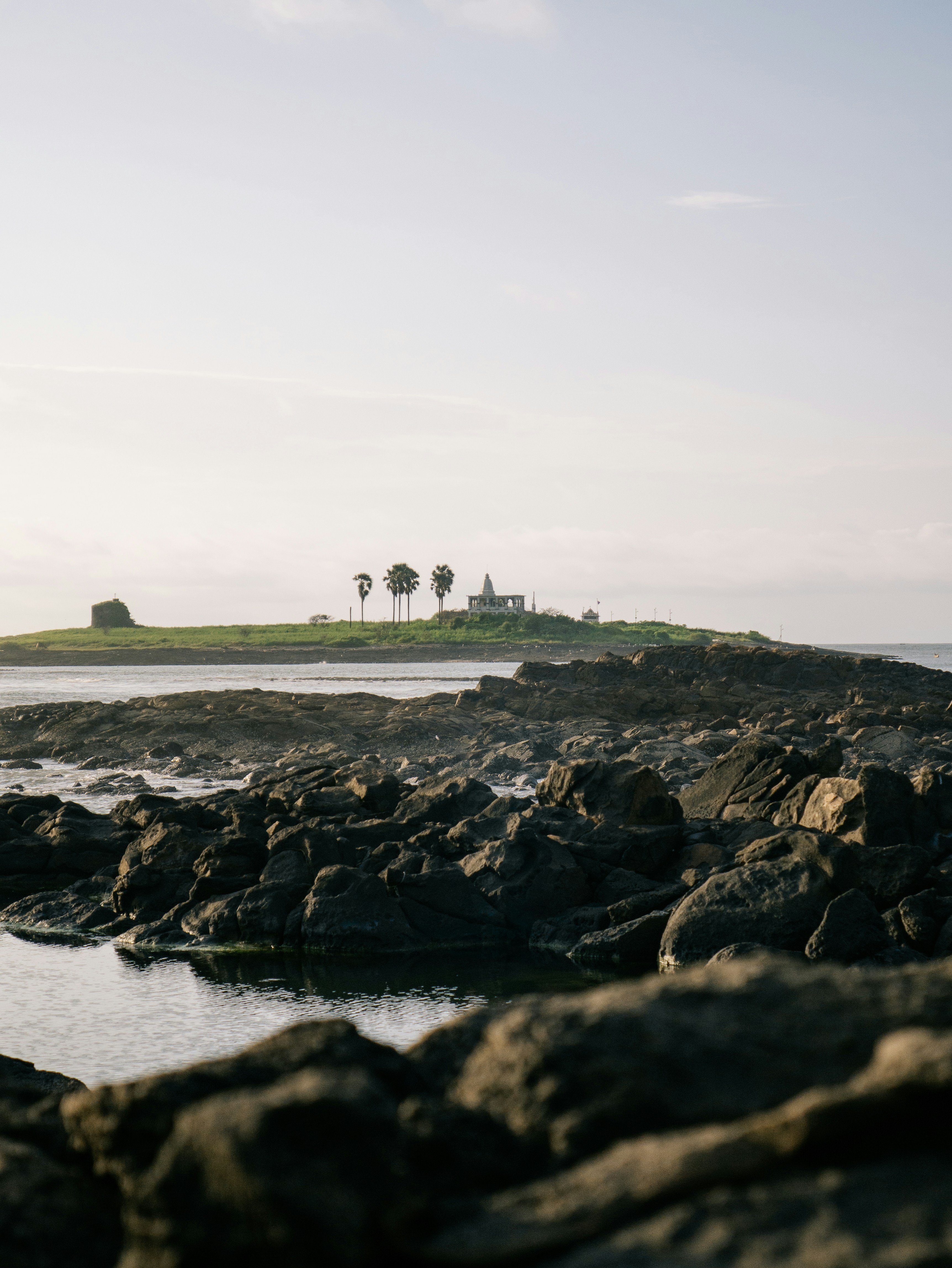 Rocky shore with island and lighthouse in distance.