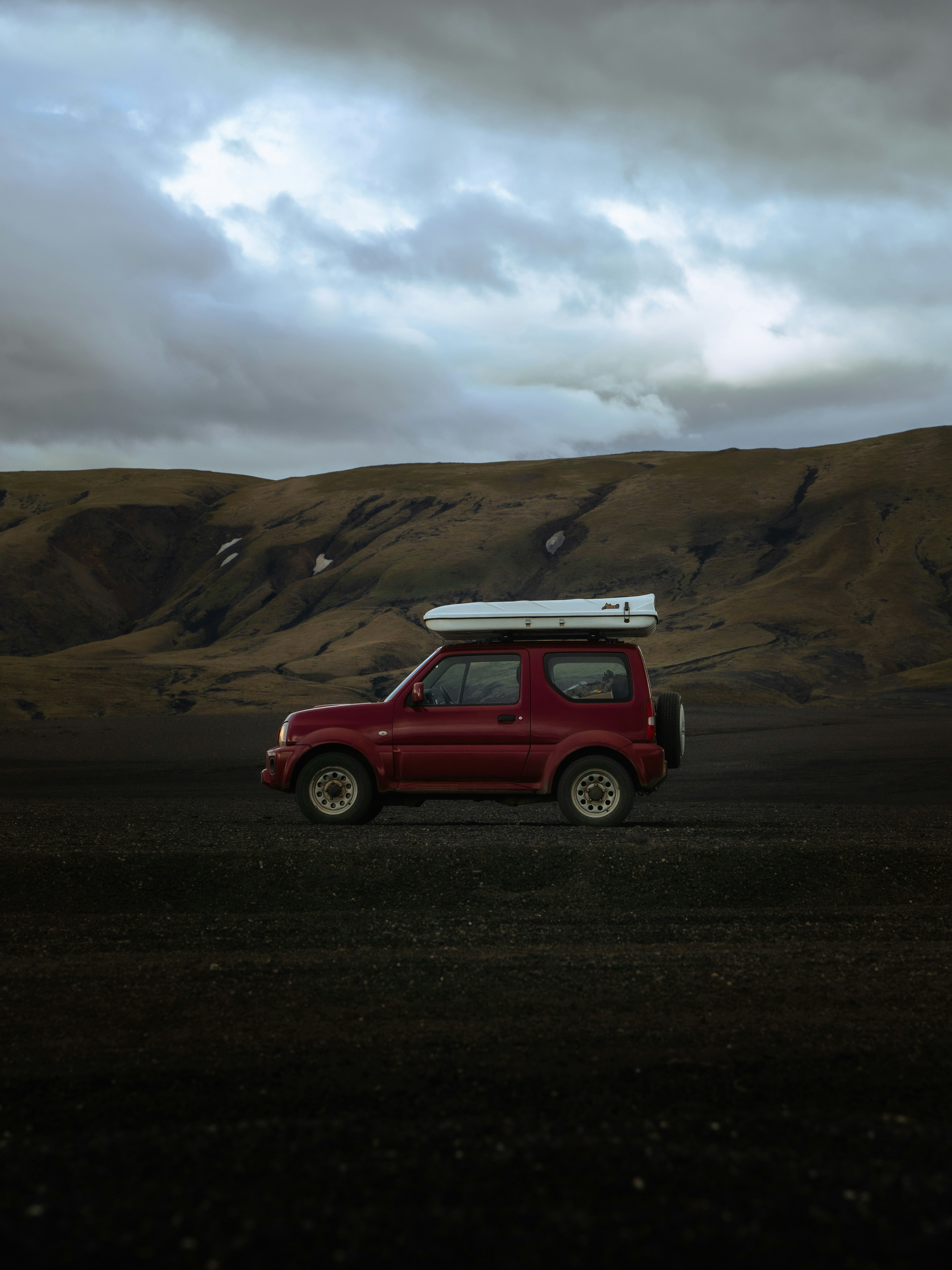 Suzuki Jimny with rooftent in Iceland | Red suv with rooftop tent parked on dark terrain.