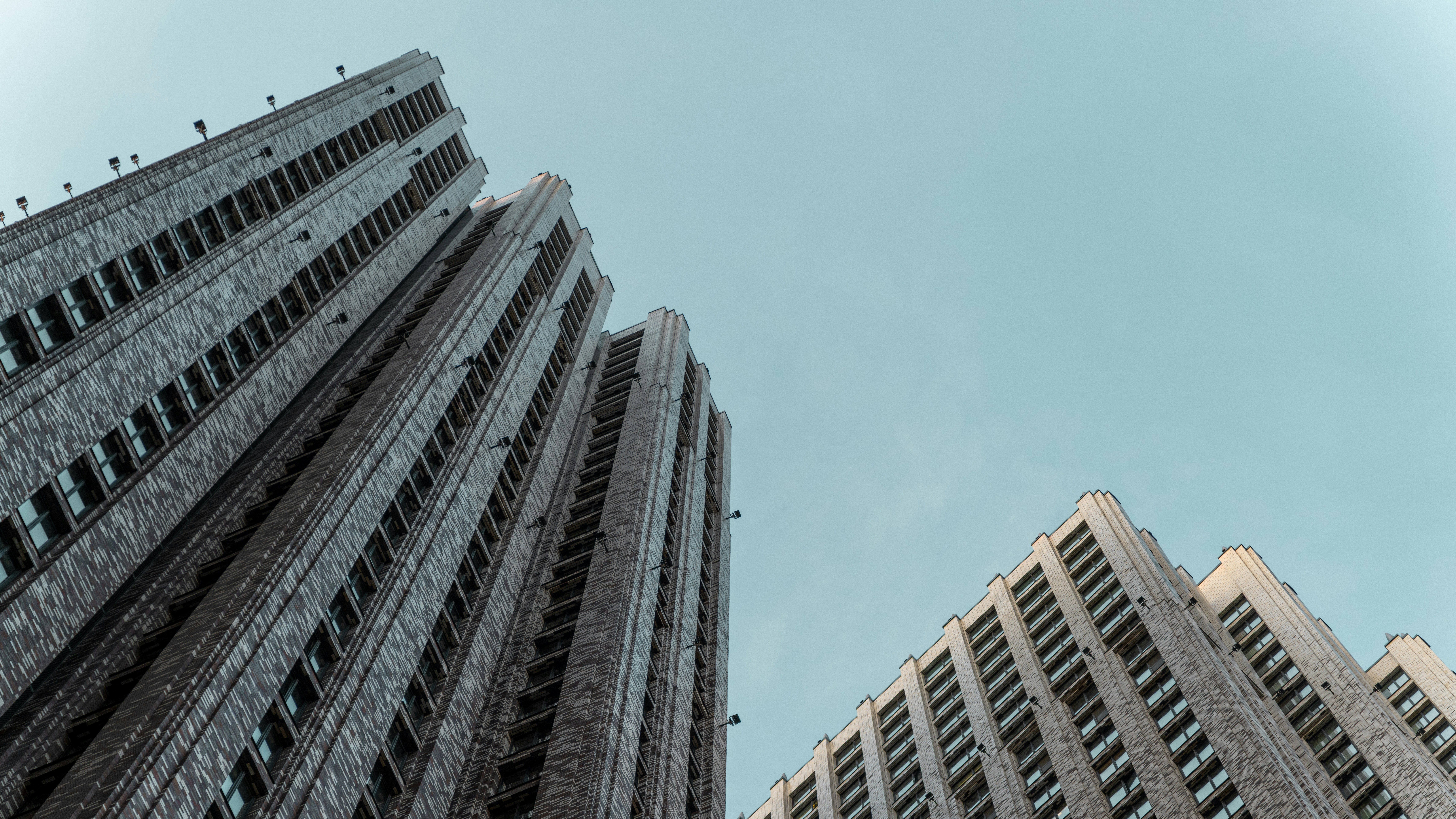 Two towering skyscrapers rise against a pale blue sky, showcasing modern architectural lines and textures.