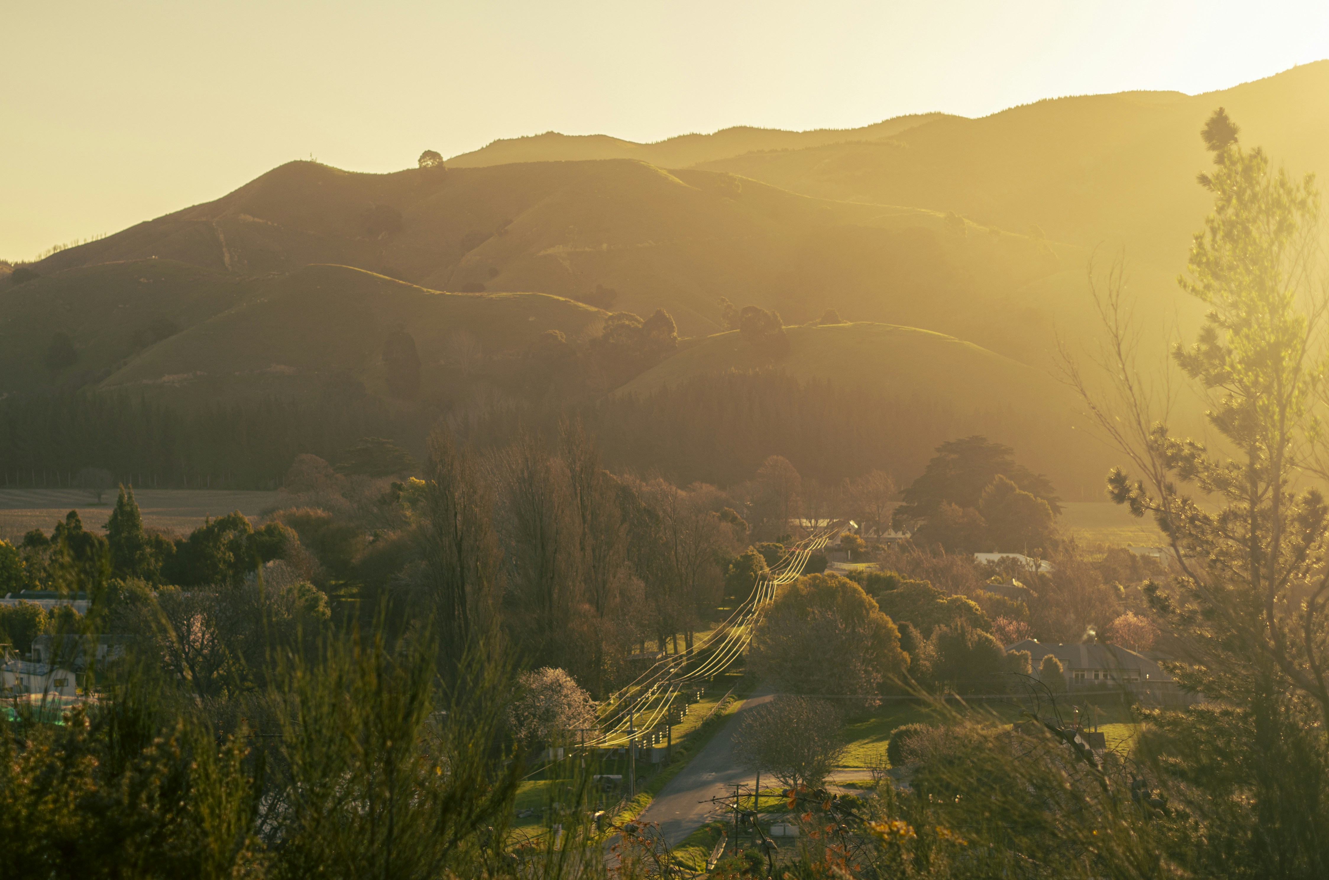 Sunlight bathes rolling hills and a serene landscape, highlighting the gentle curves and textures of nature. The scene captures a tranquil moment at dusk.