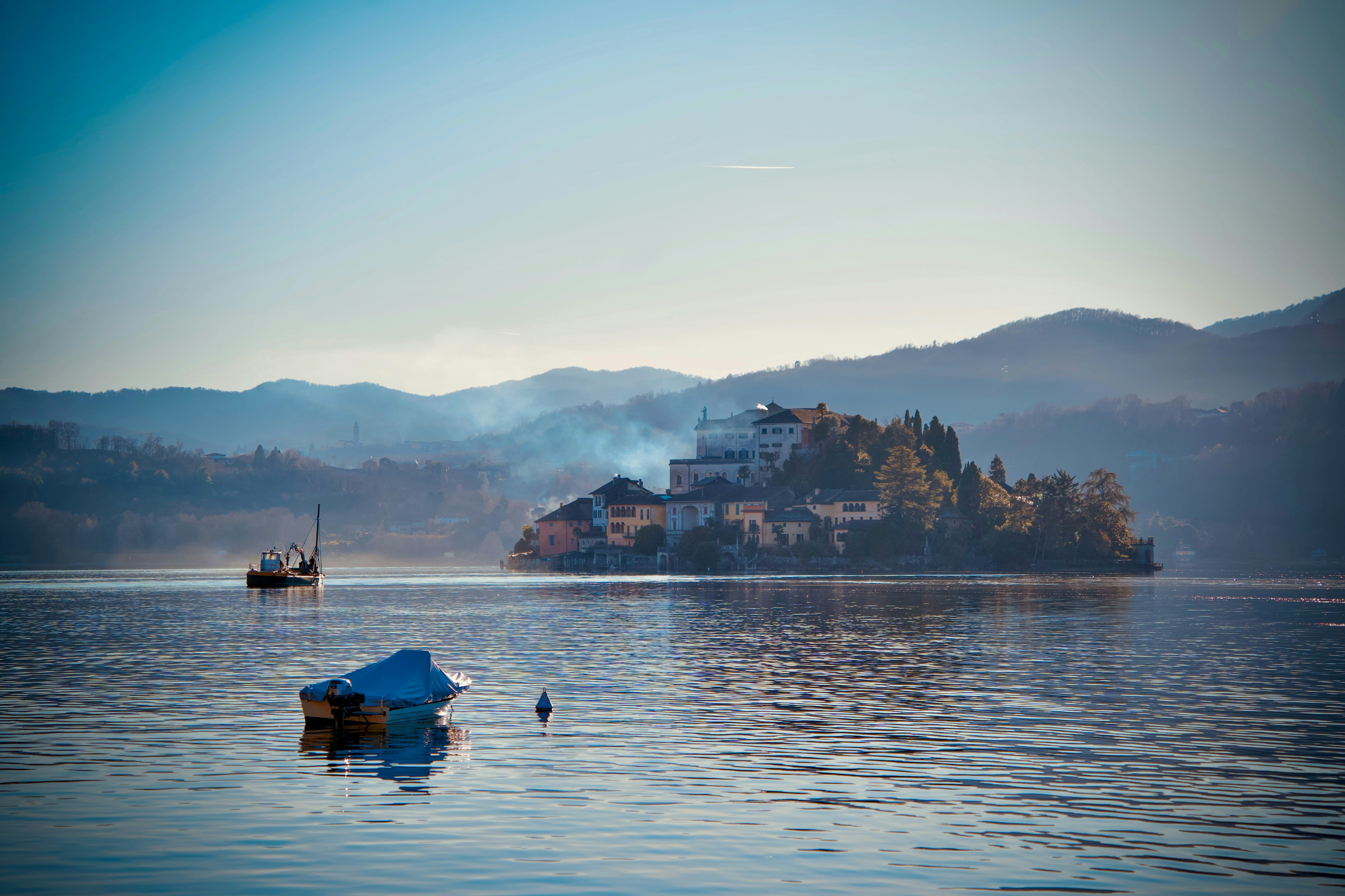 A tranquil lakeside scene featuring a small boat in the foreground and a quaint island village nestled among rolling hills in the background.