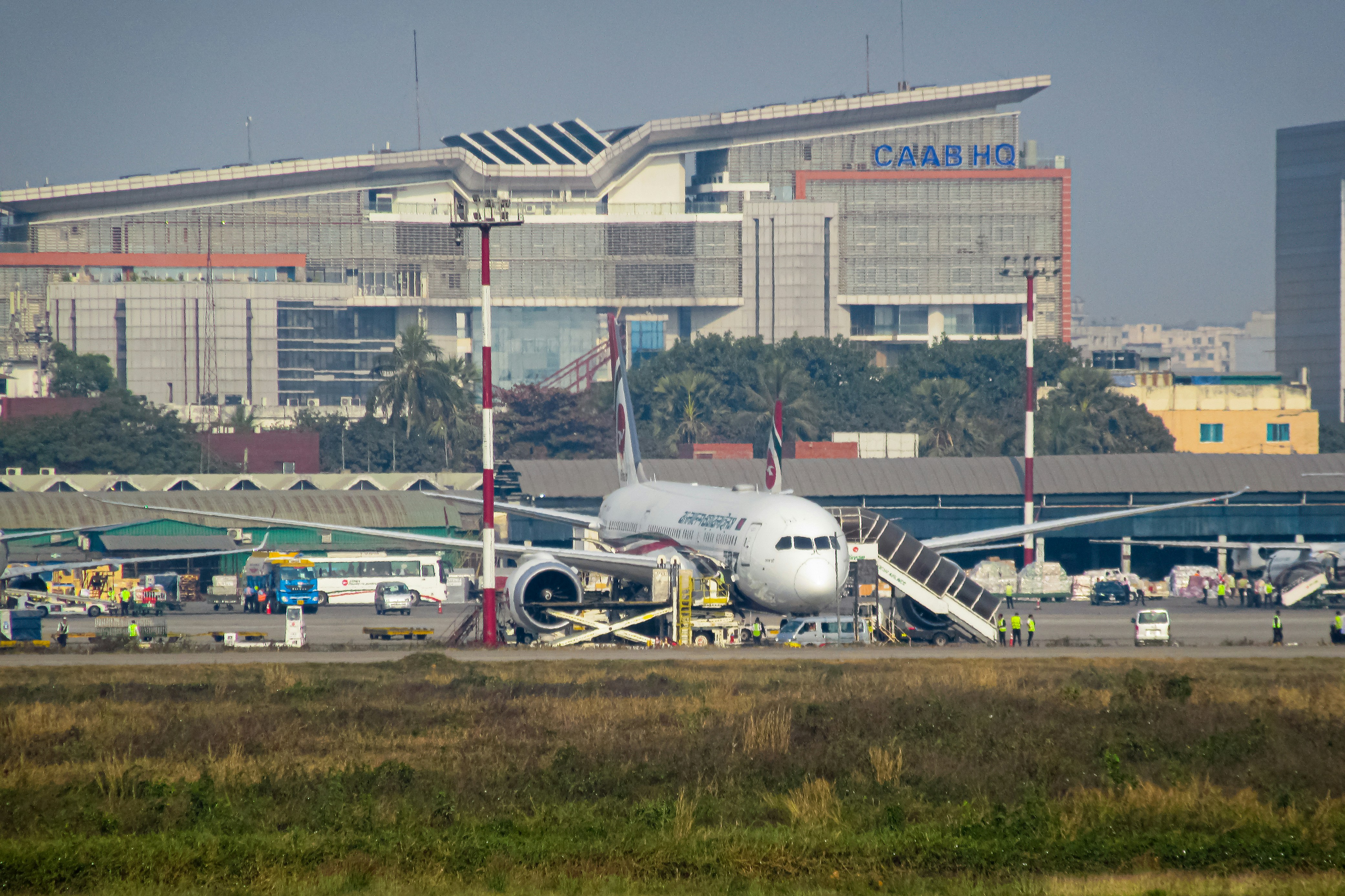 Airplane being serviced at an airport terminal with ground crew and equipment visible. The modern terminal building looms in the background.