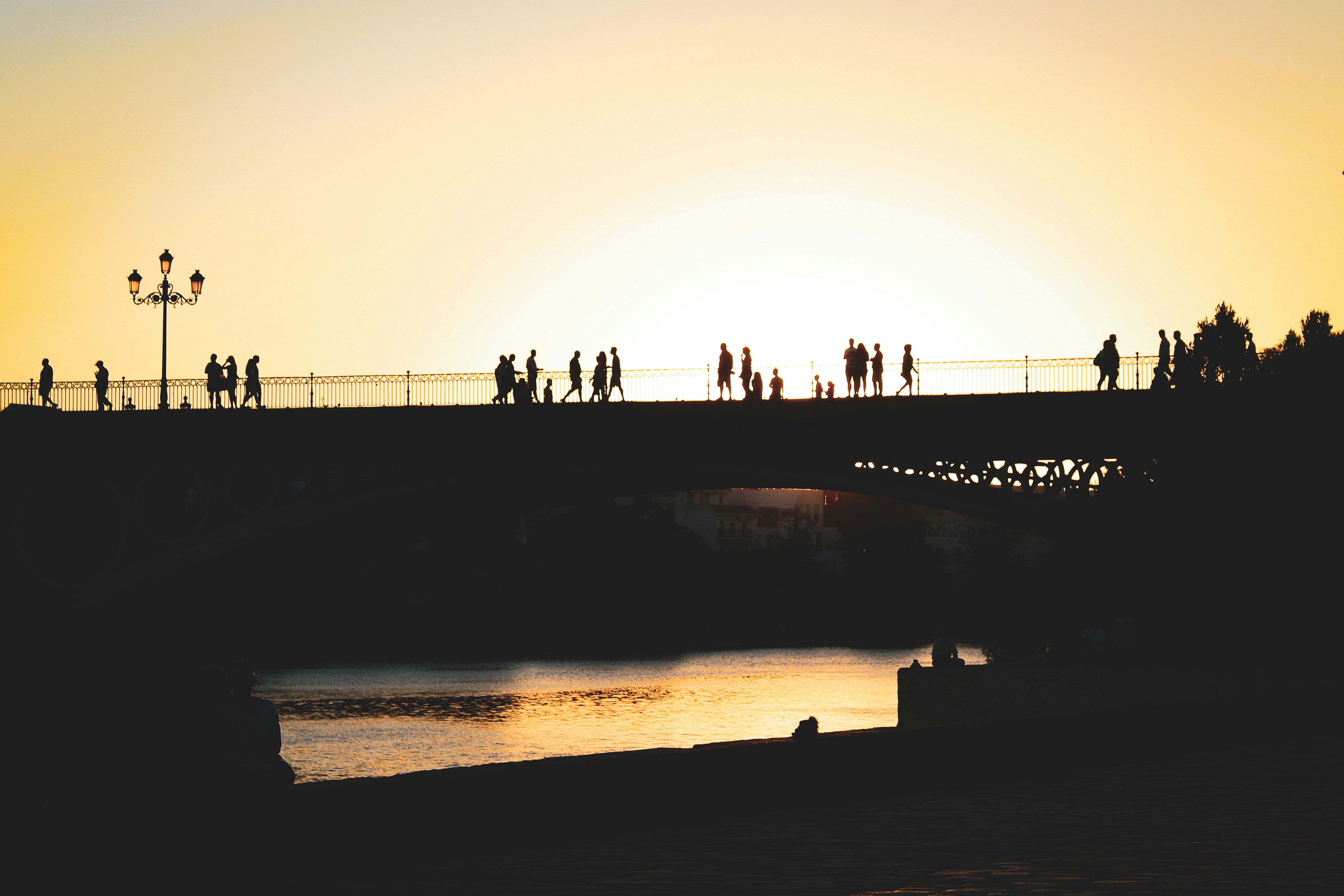 Silhouettes of people walking on a bridge at sunset.