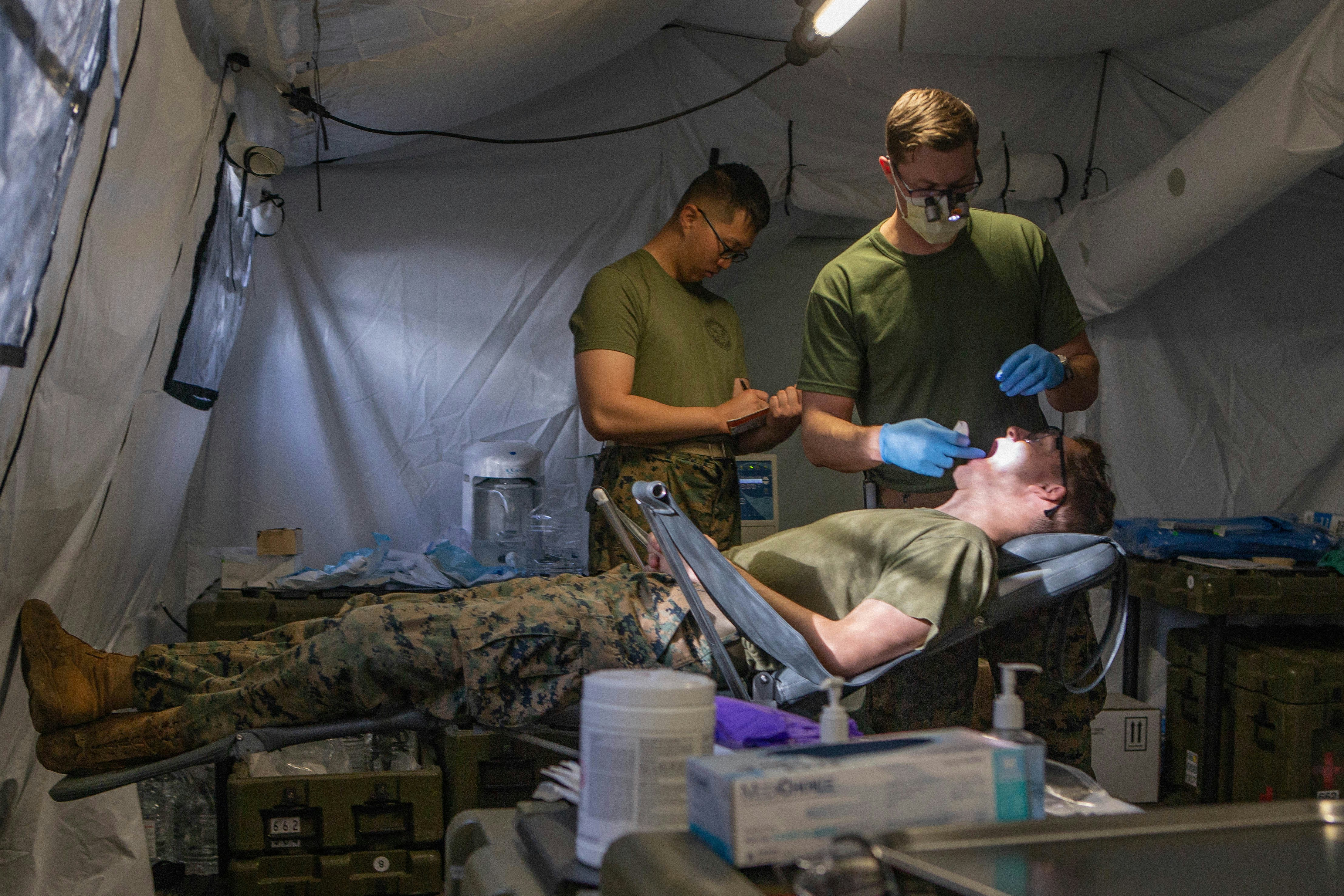 Two military personnel provide dental care in a field tent, showcasing the importance of medical support in remote locations.