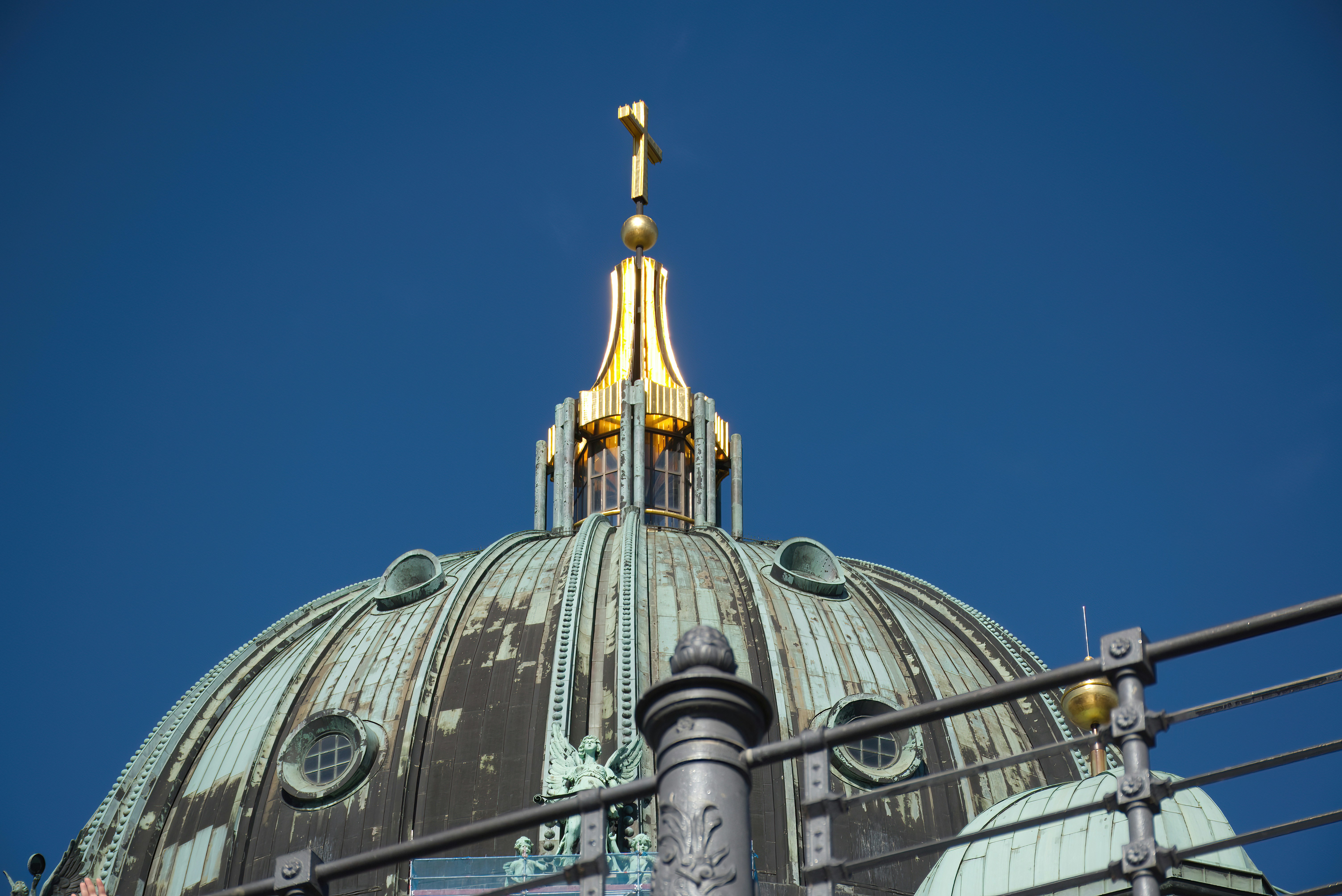 The ornate dome of a grand building, crowned with a golden cross, stands against a clear blue sky.