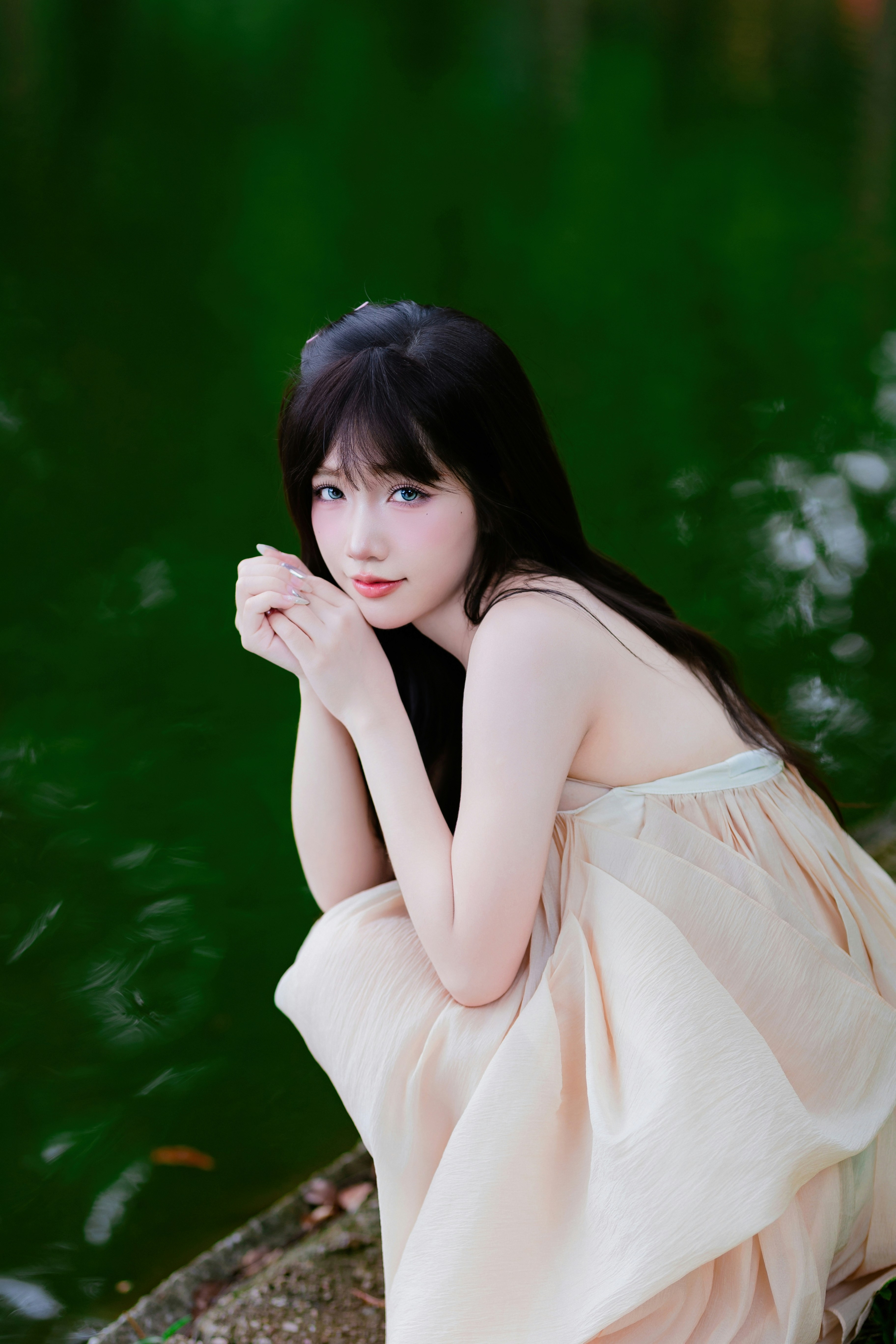 A young woman in a flowing dress gazes thoughtfully while seated beside a tranquil green lake, capturing a moment of introspection.