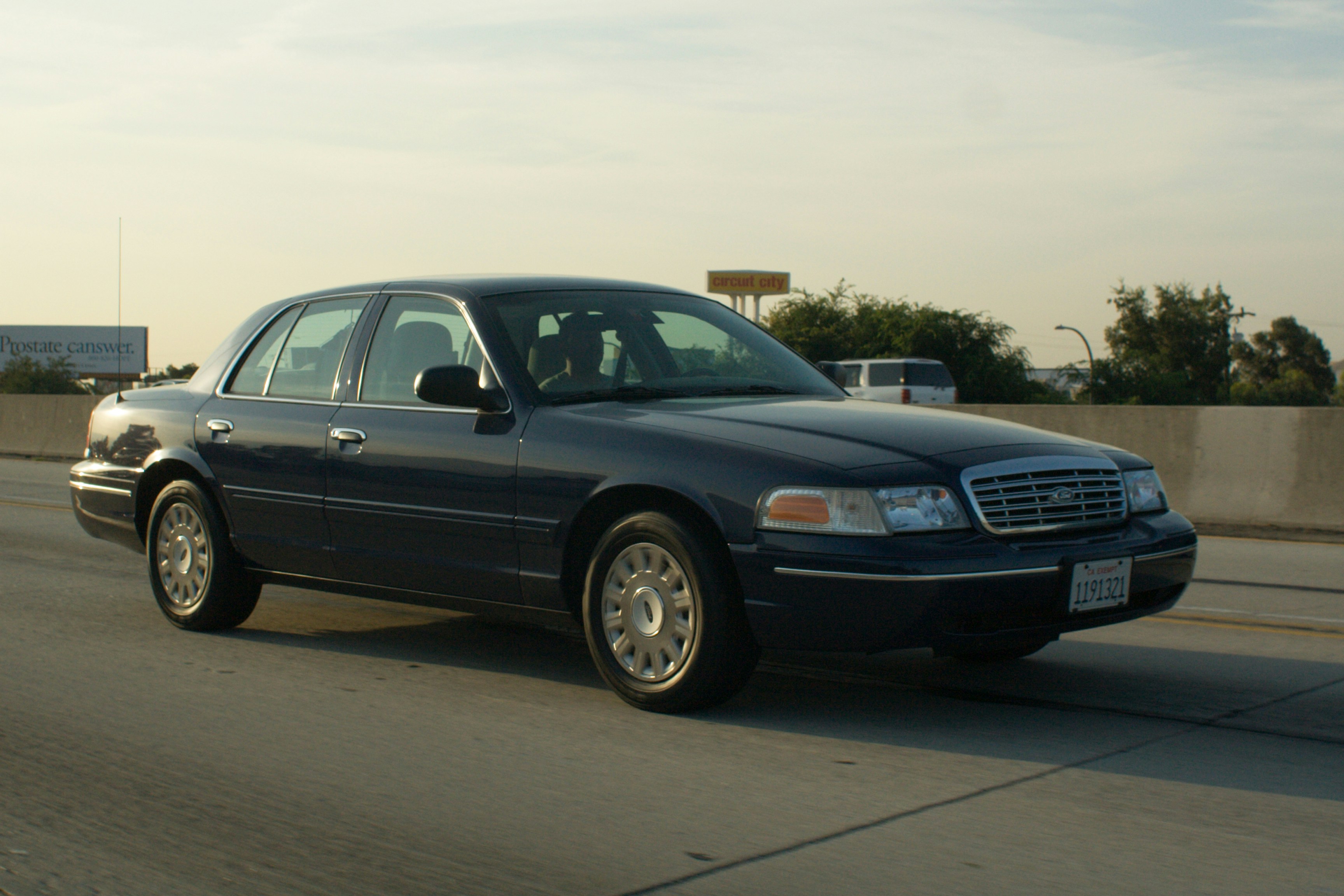 A blue sedan gliding along a highway, illuminated by the warm glow of the setting sun.