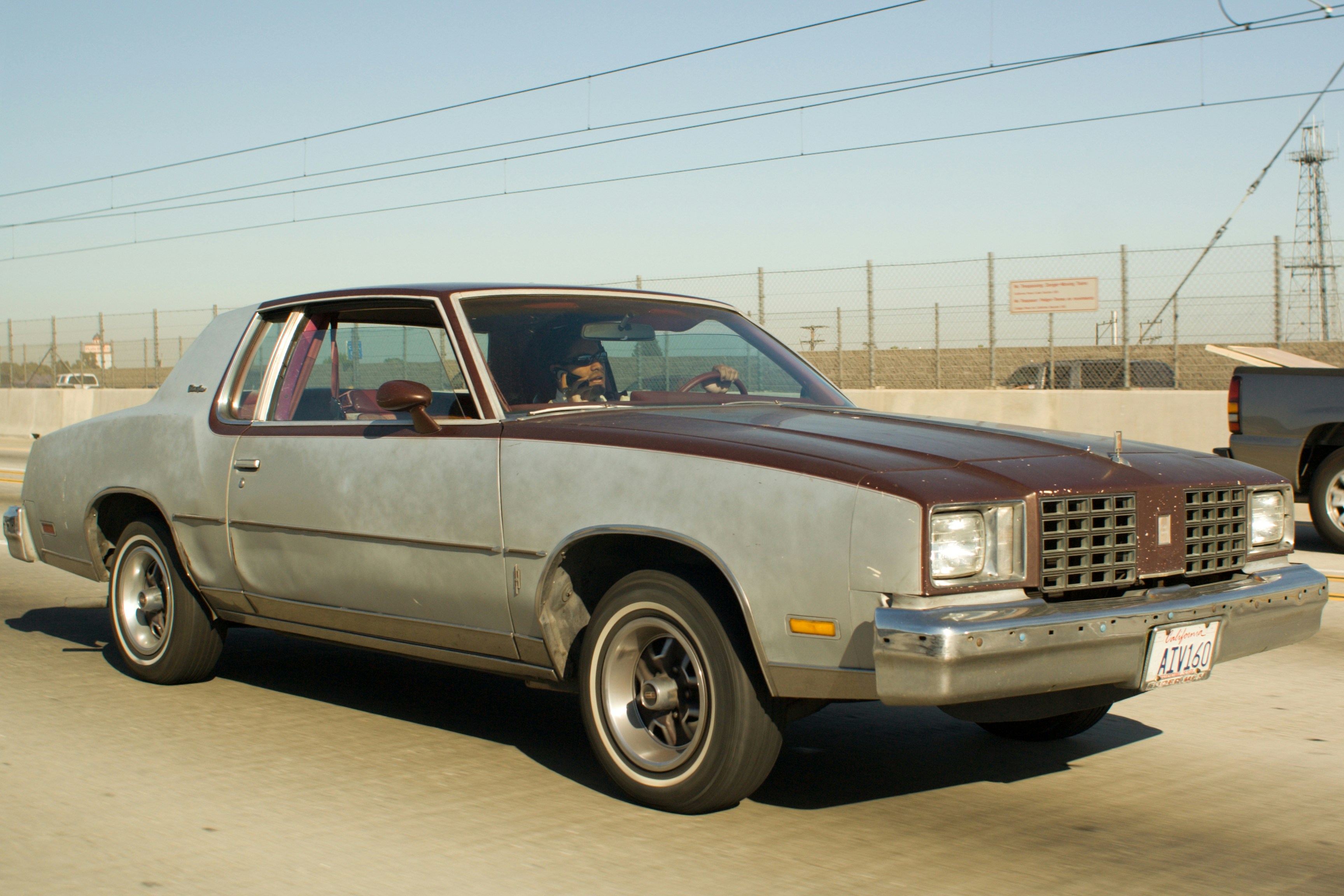 A classic car with a faded exterior glides along a highway, showcasing its retro design and character. The scene captures a moment of automotive nostalgia.