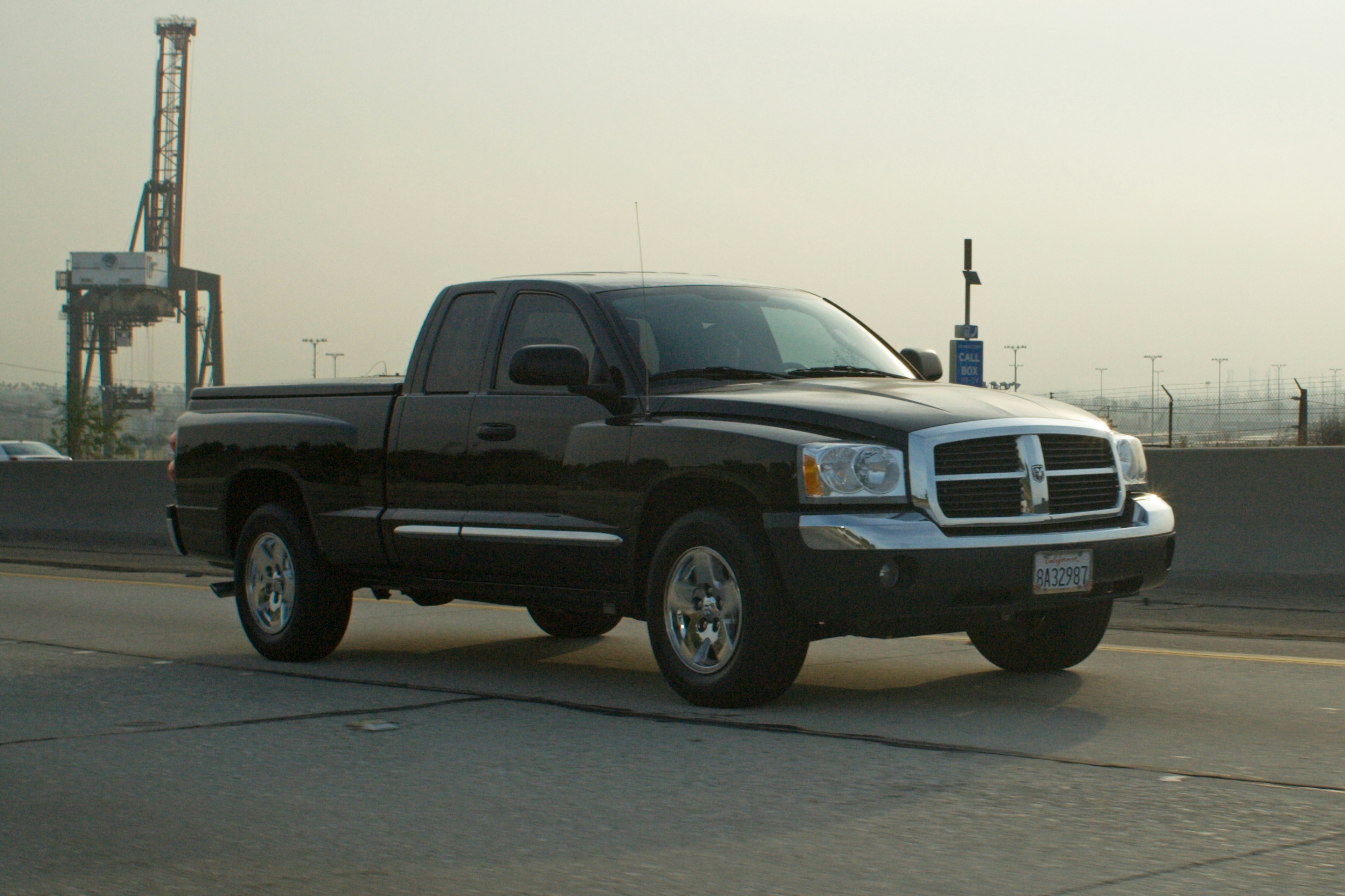 A black pickup truck cruising along a highway with an industrial backdrop, showcasing the blend of urban life and transportation. 