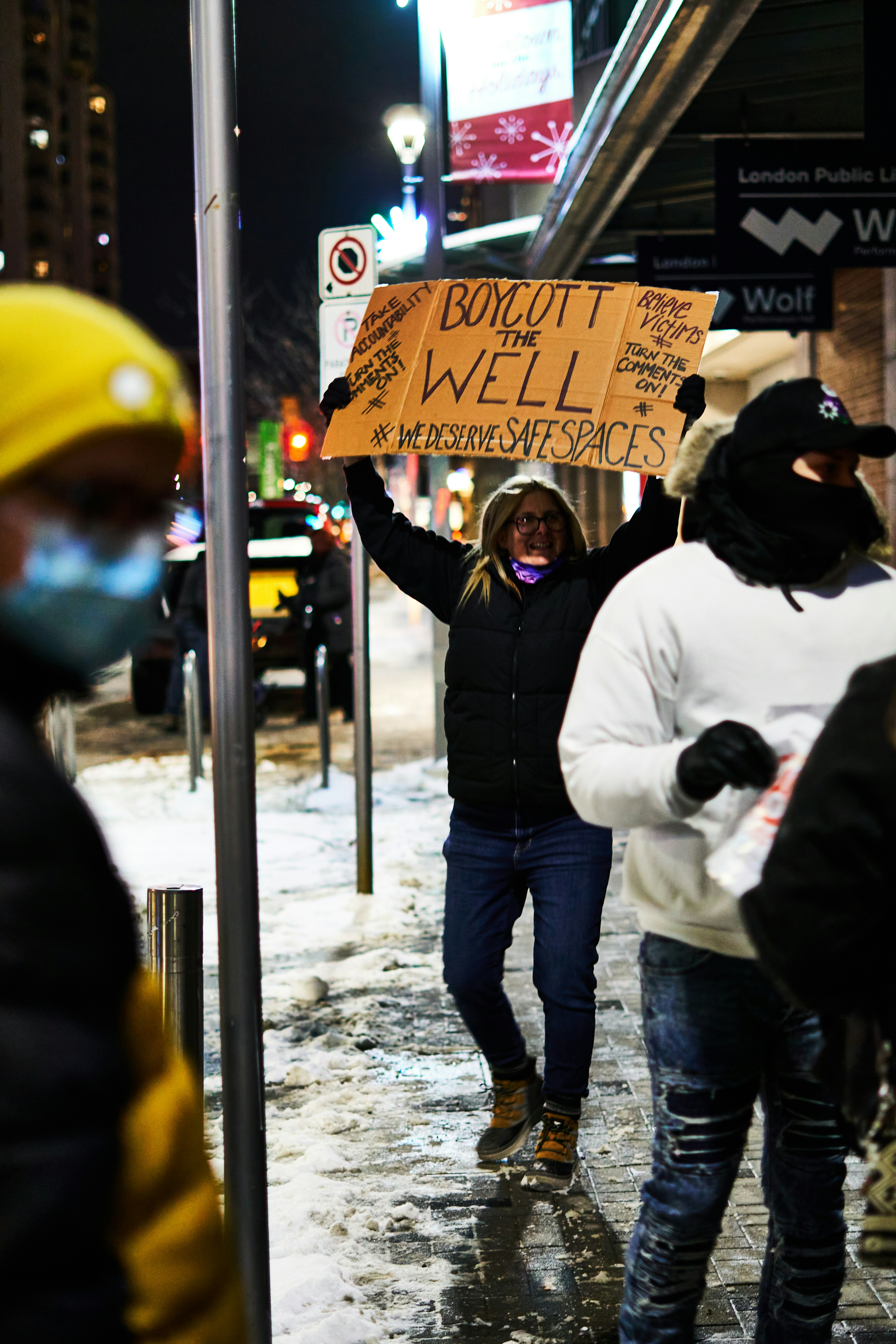 Protester holds sign reading "boycott the well" on snowy street.
