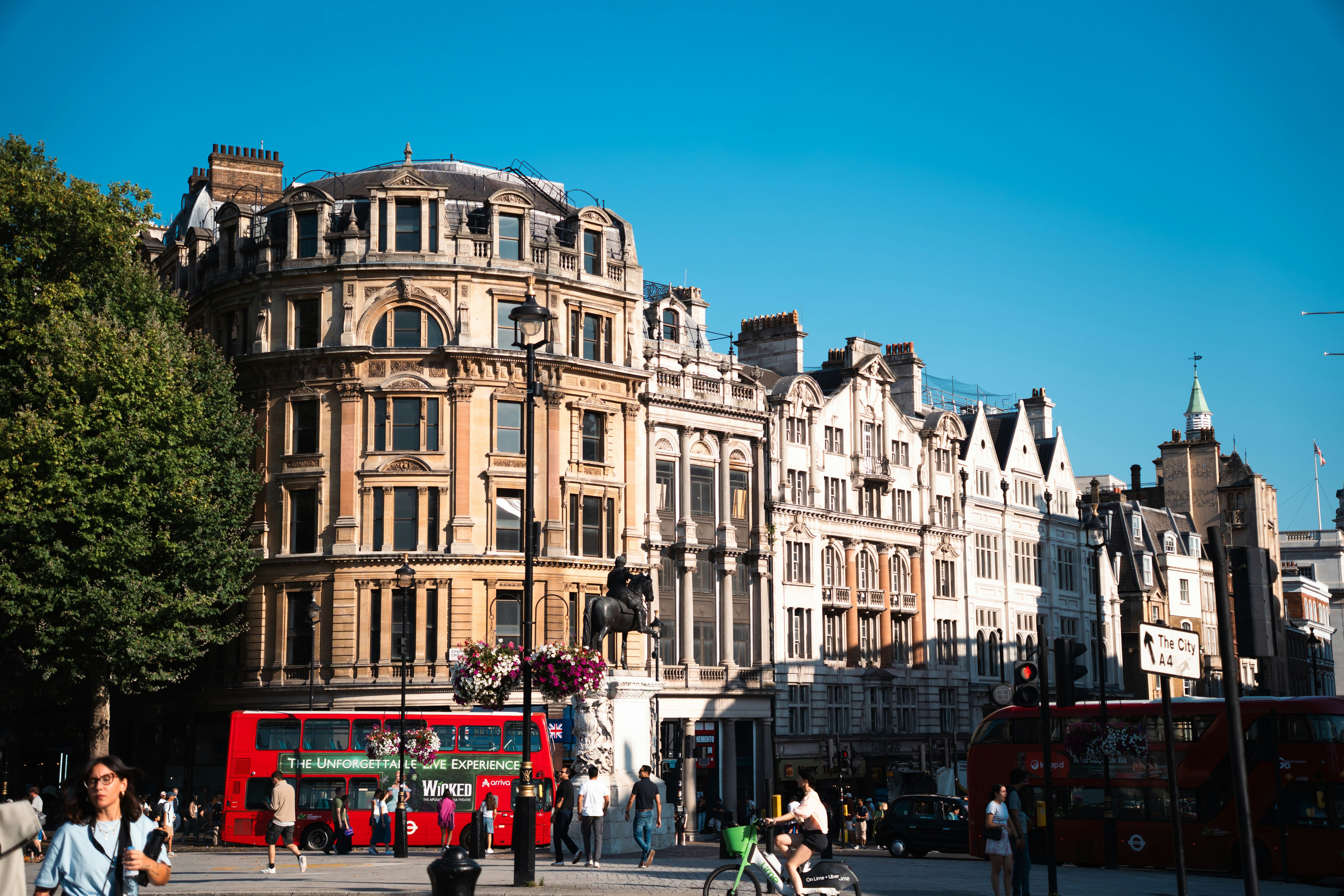 Sunny Trafalgar Square scene with classic London architecture and iconic red double-decker bus | Red double-decker bus on a city street with buildings.