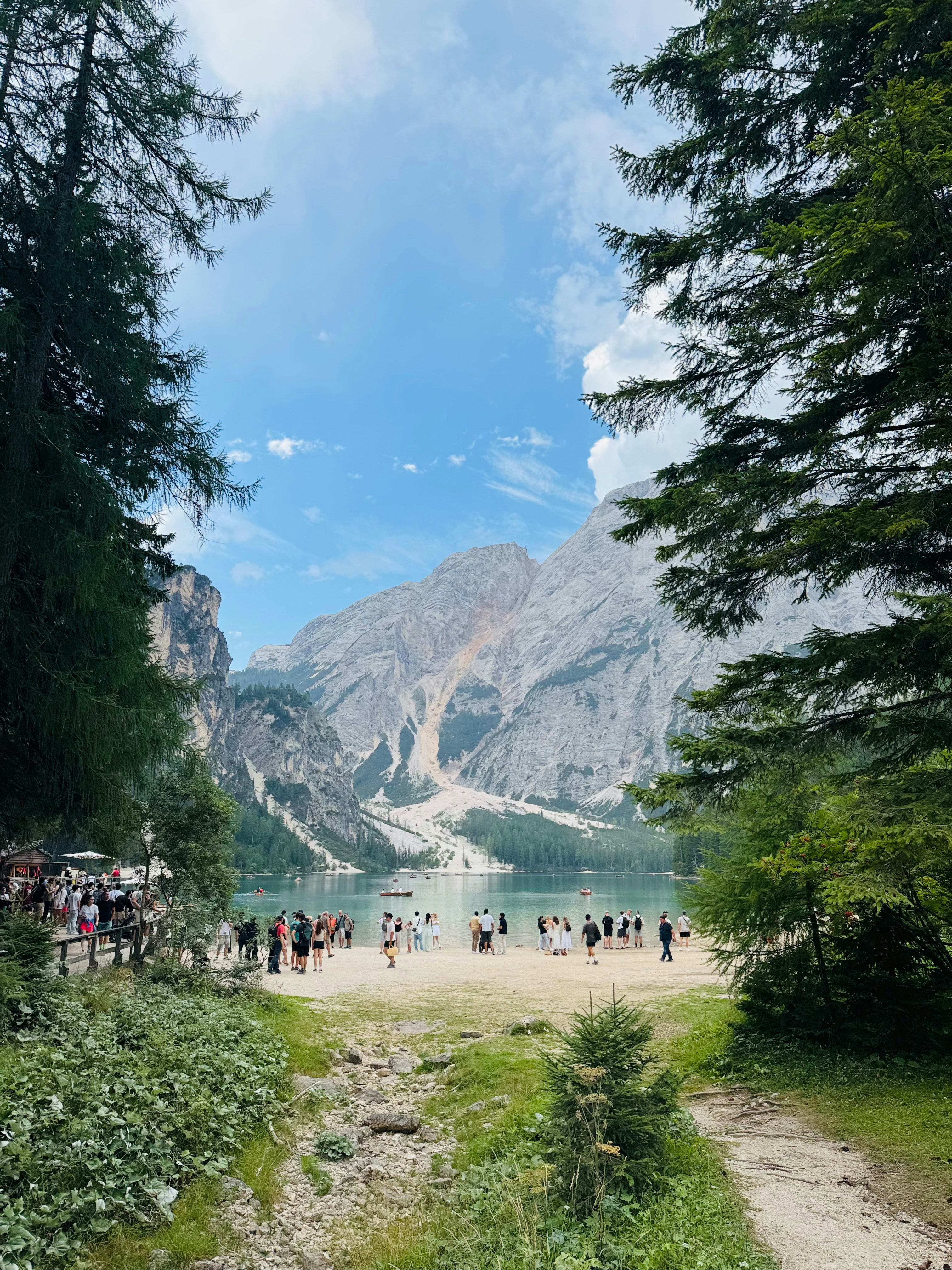 Visitors gathering along the sandy shore of a tranquil lake surrounded by towering mountains and lush trees.