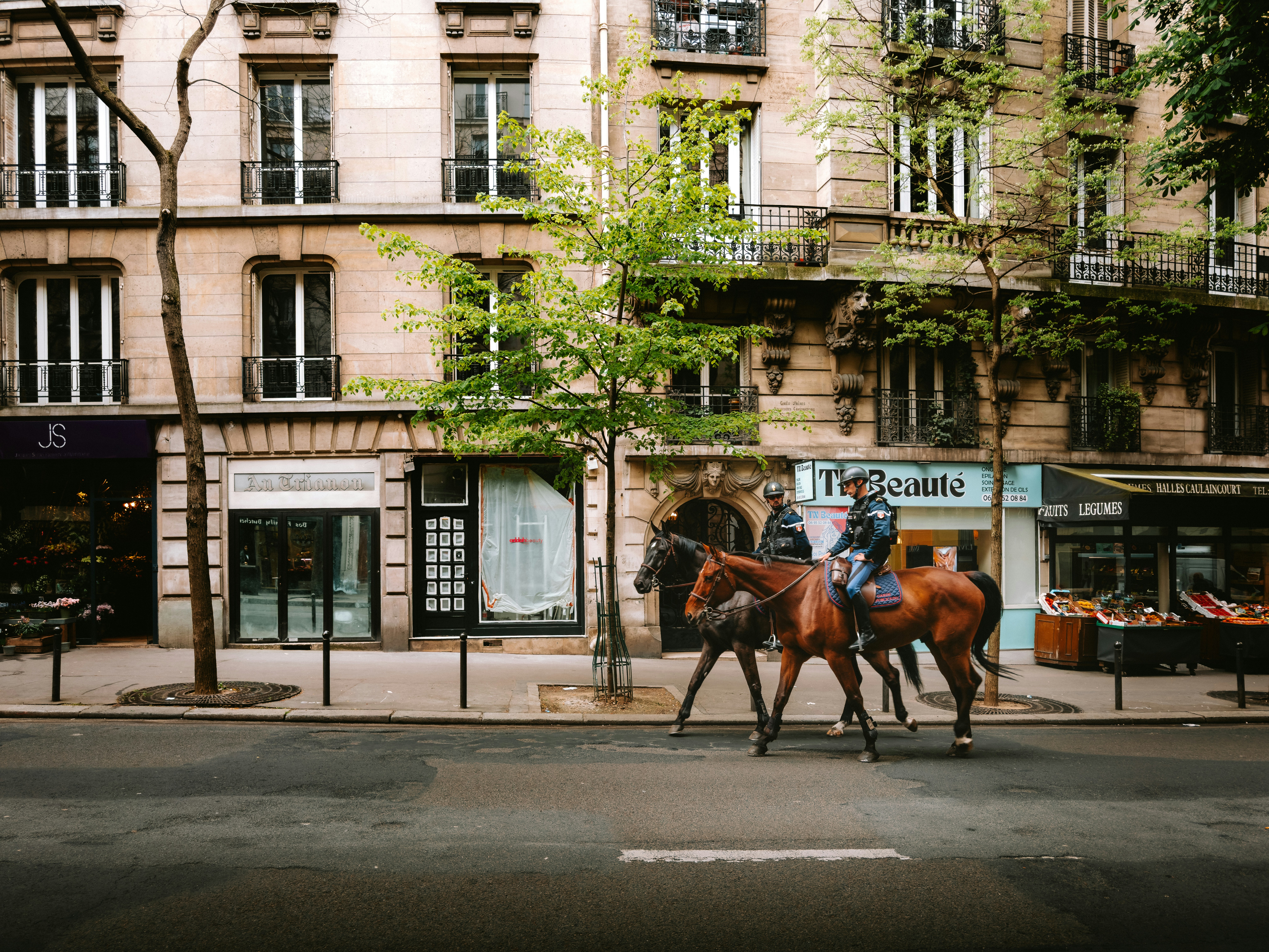 Two people riding horses on a city street.
