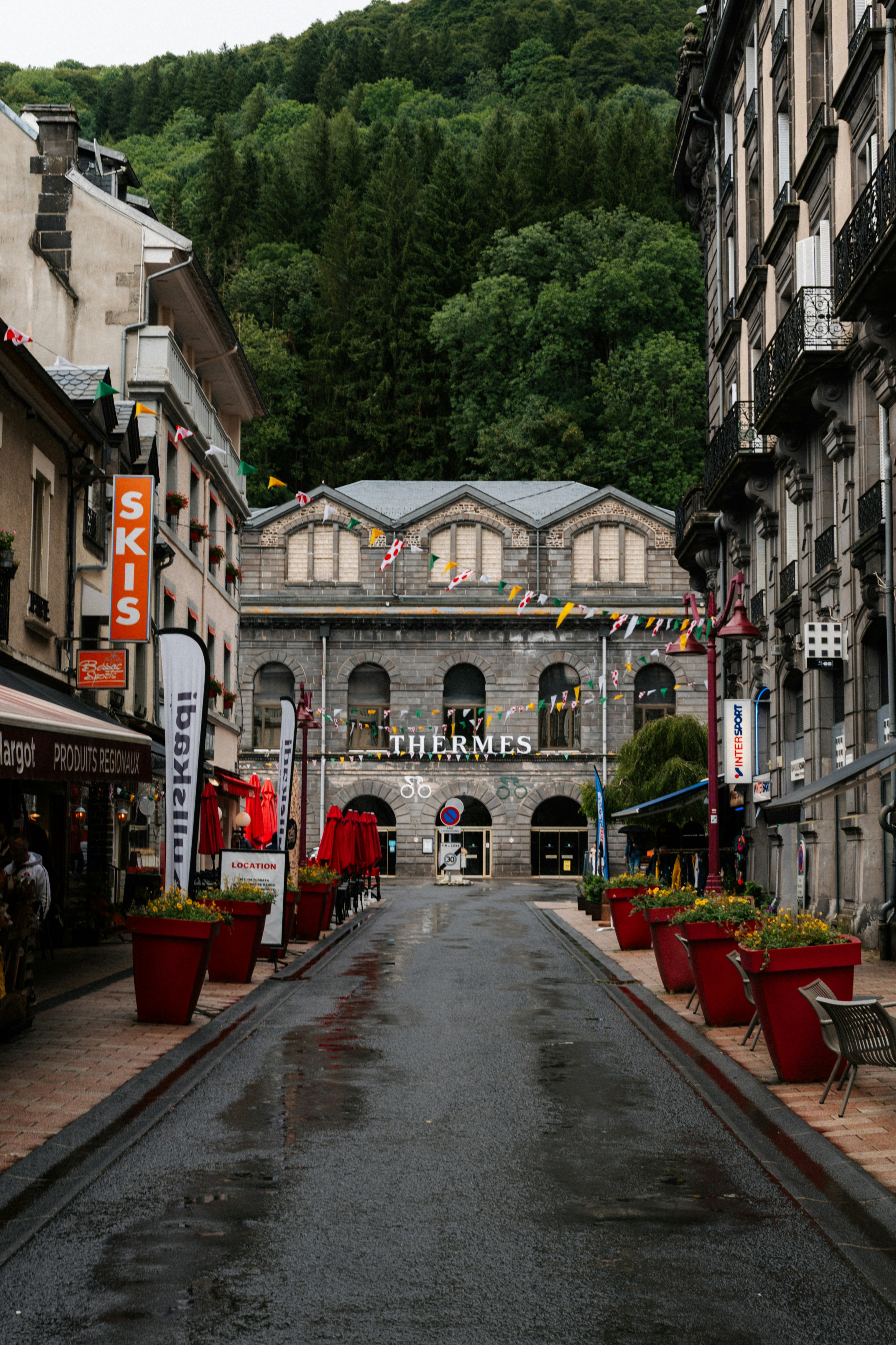 Wet street leading to a stone building with 'thermes' sign.