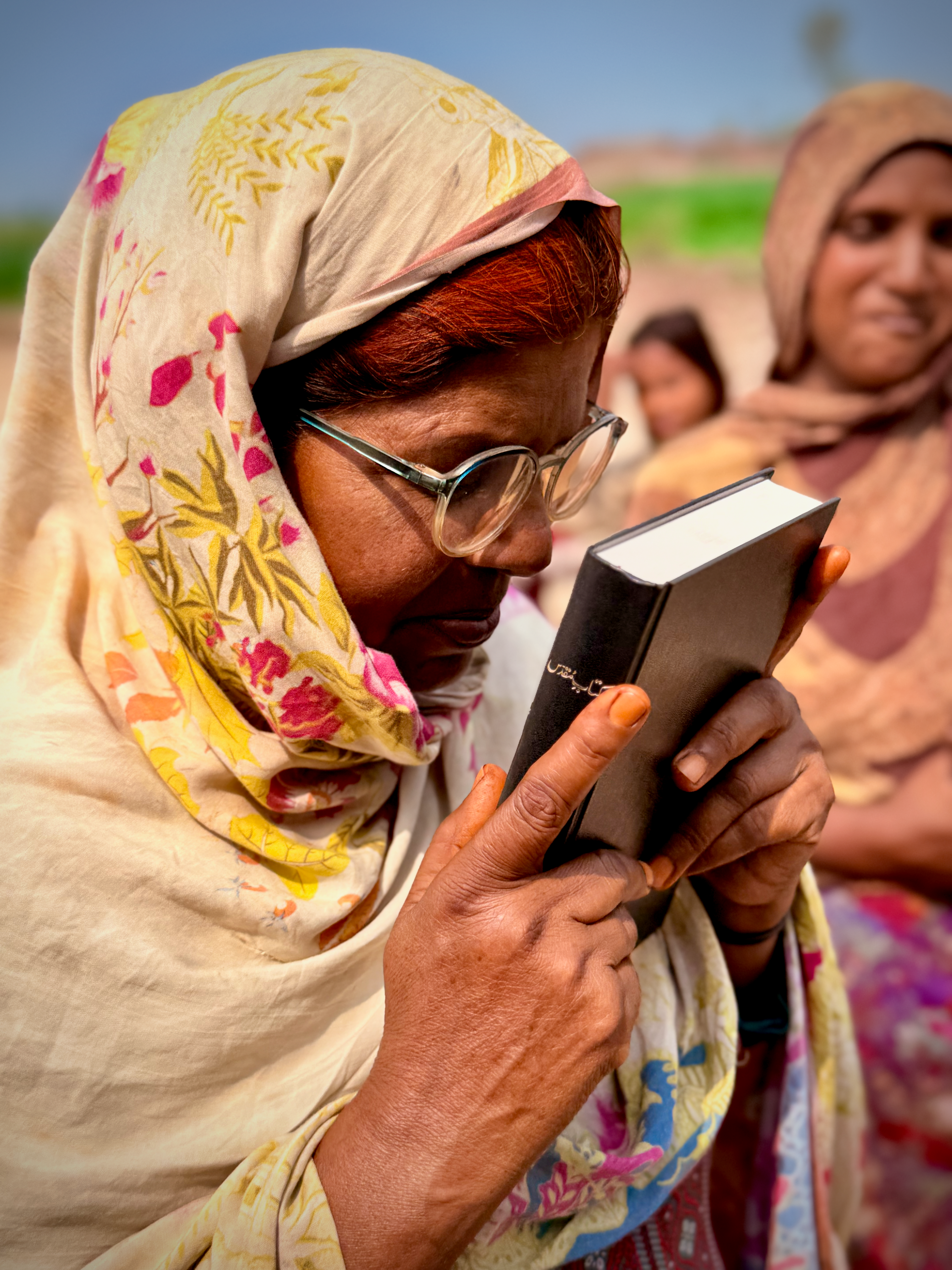 Woman wearing glasses and headscarf reads a book.