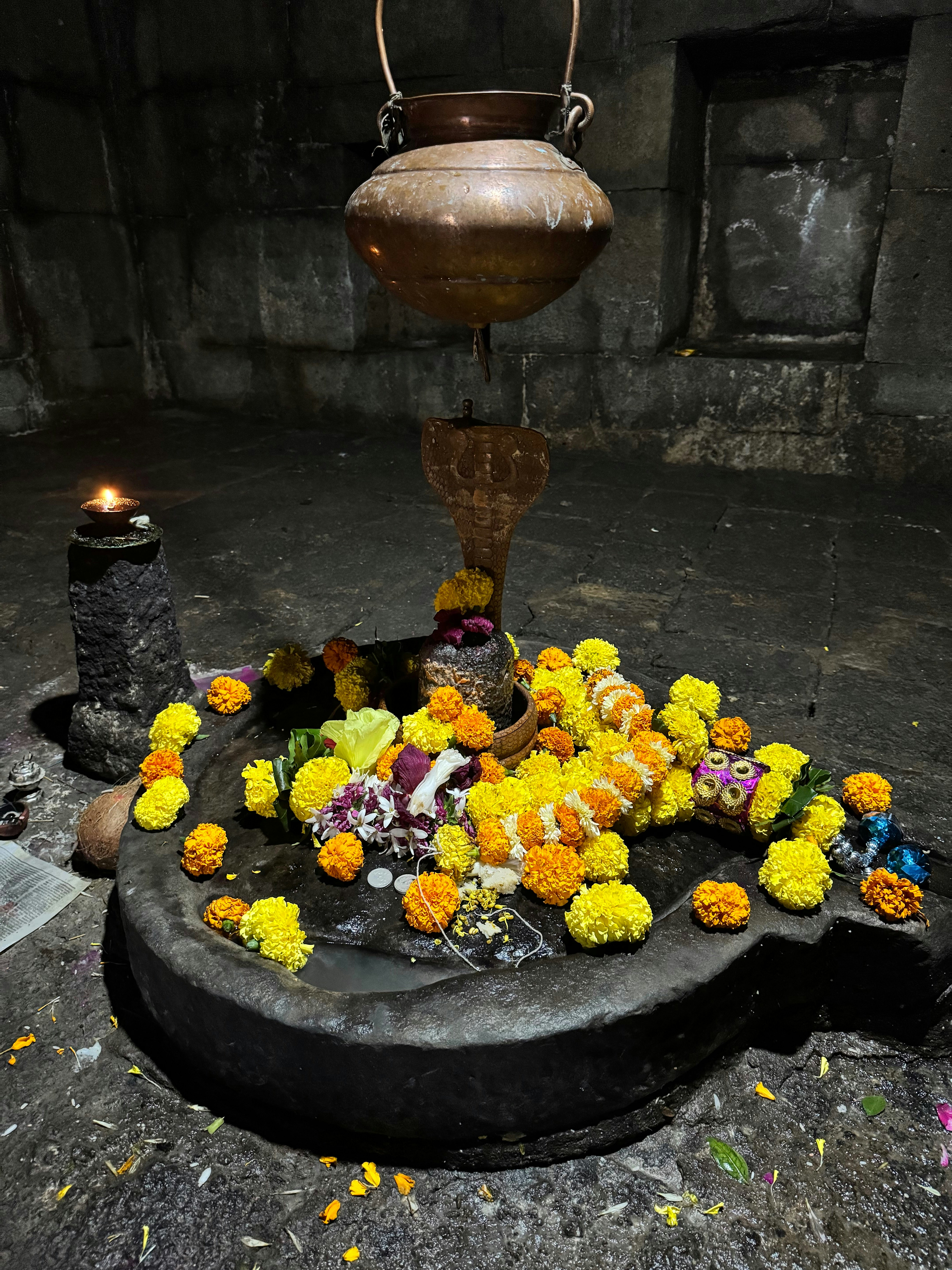 Shiva lingam adorned with flowers and a snake statue.