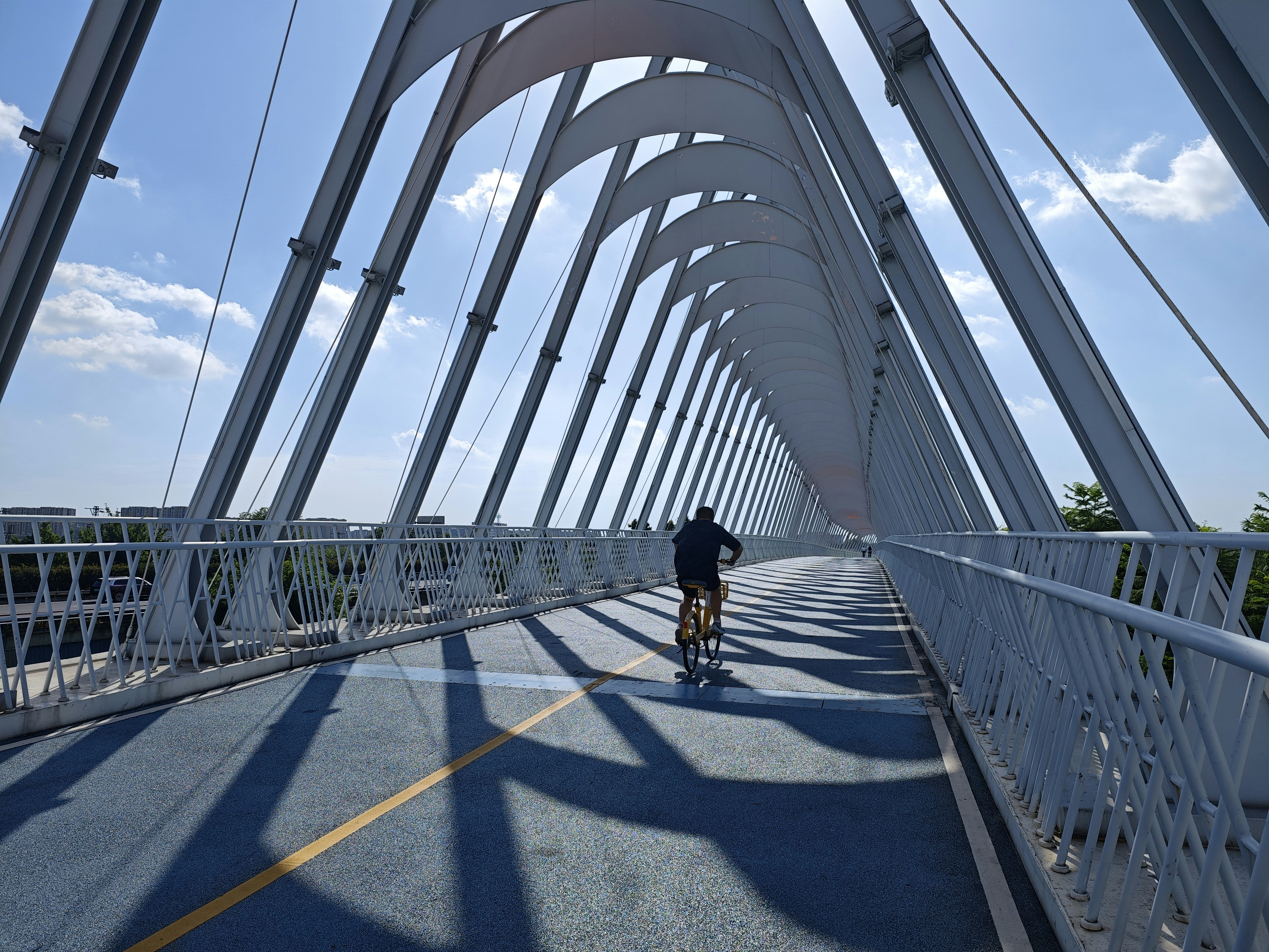 Person cycling on a modern bridge under sunlight.