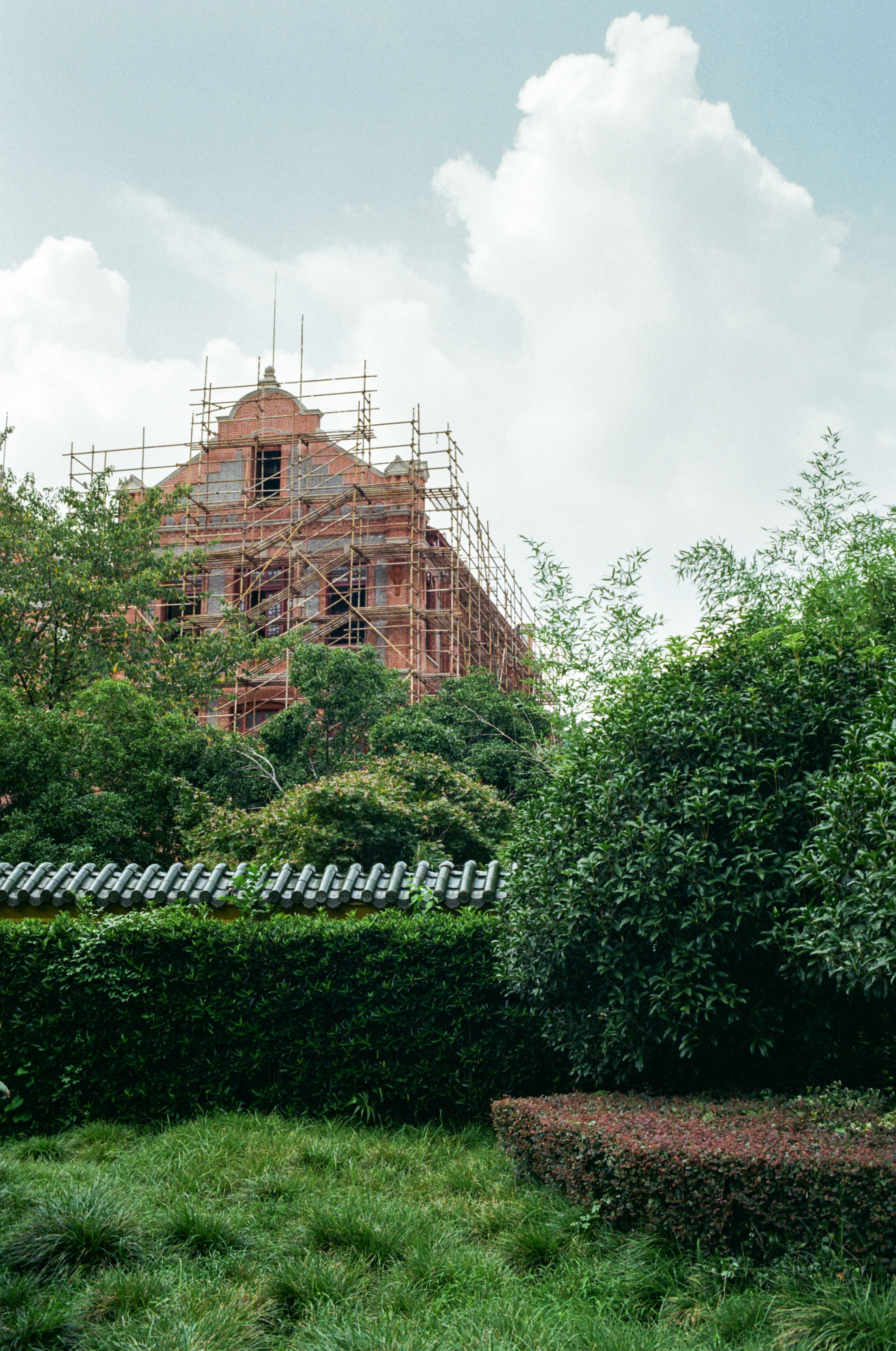 Historic building undergoing restoration, surrounded by lush greenery and traditional landscaping.