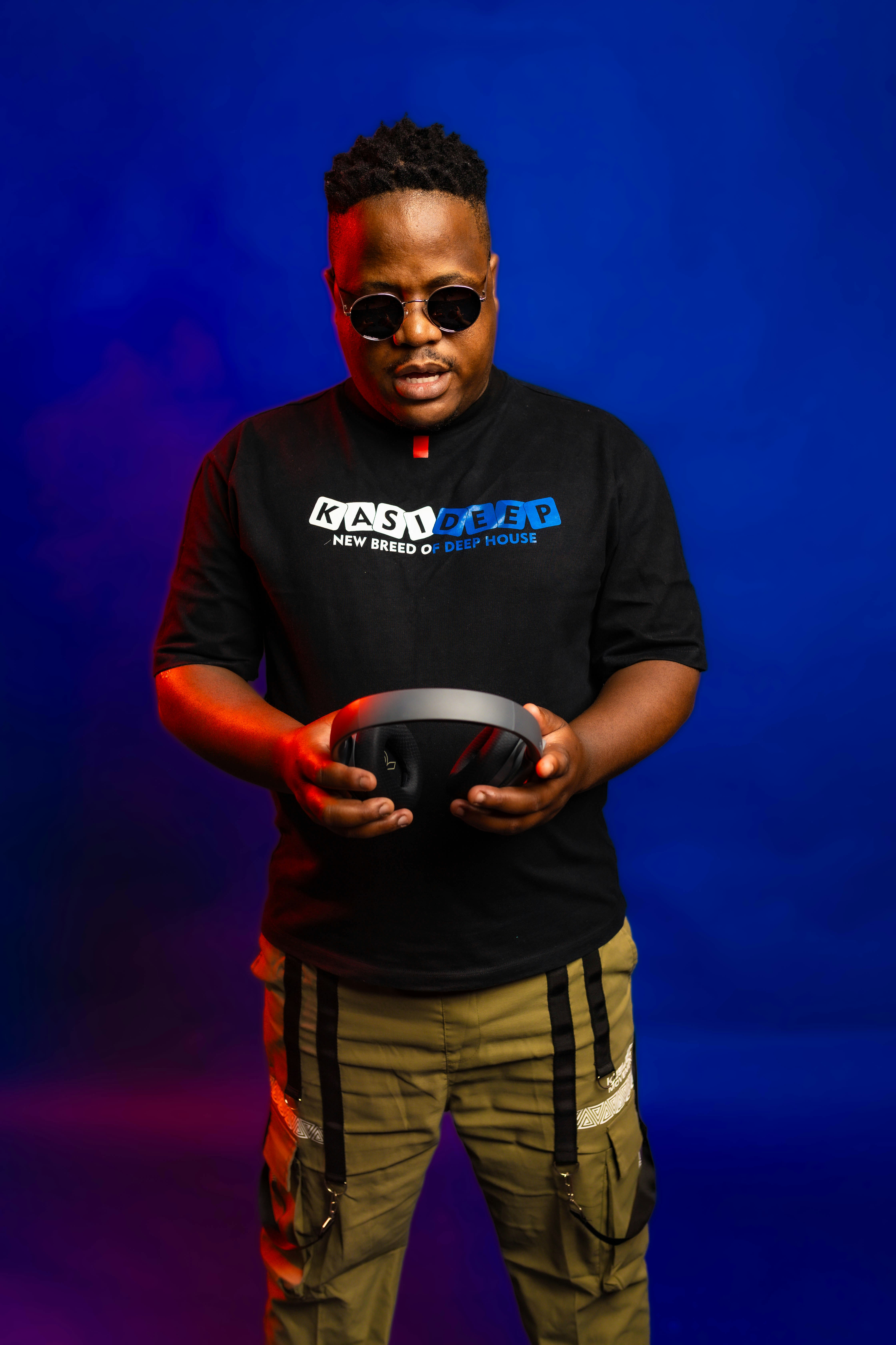 DJ Tears PLK, KasiDeep | Man in sunglasses holding headphones against blue background.