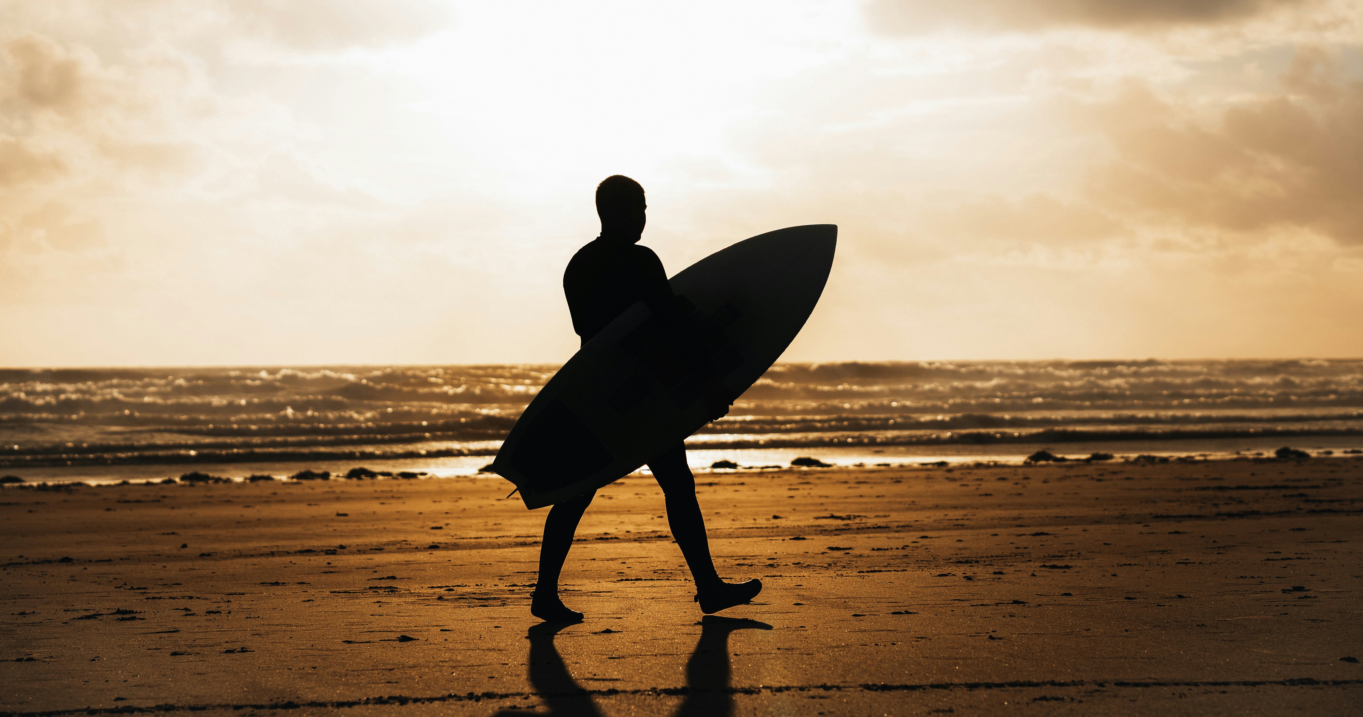 Silhouette of surfer walking on beach at sunset