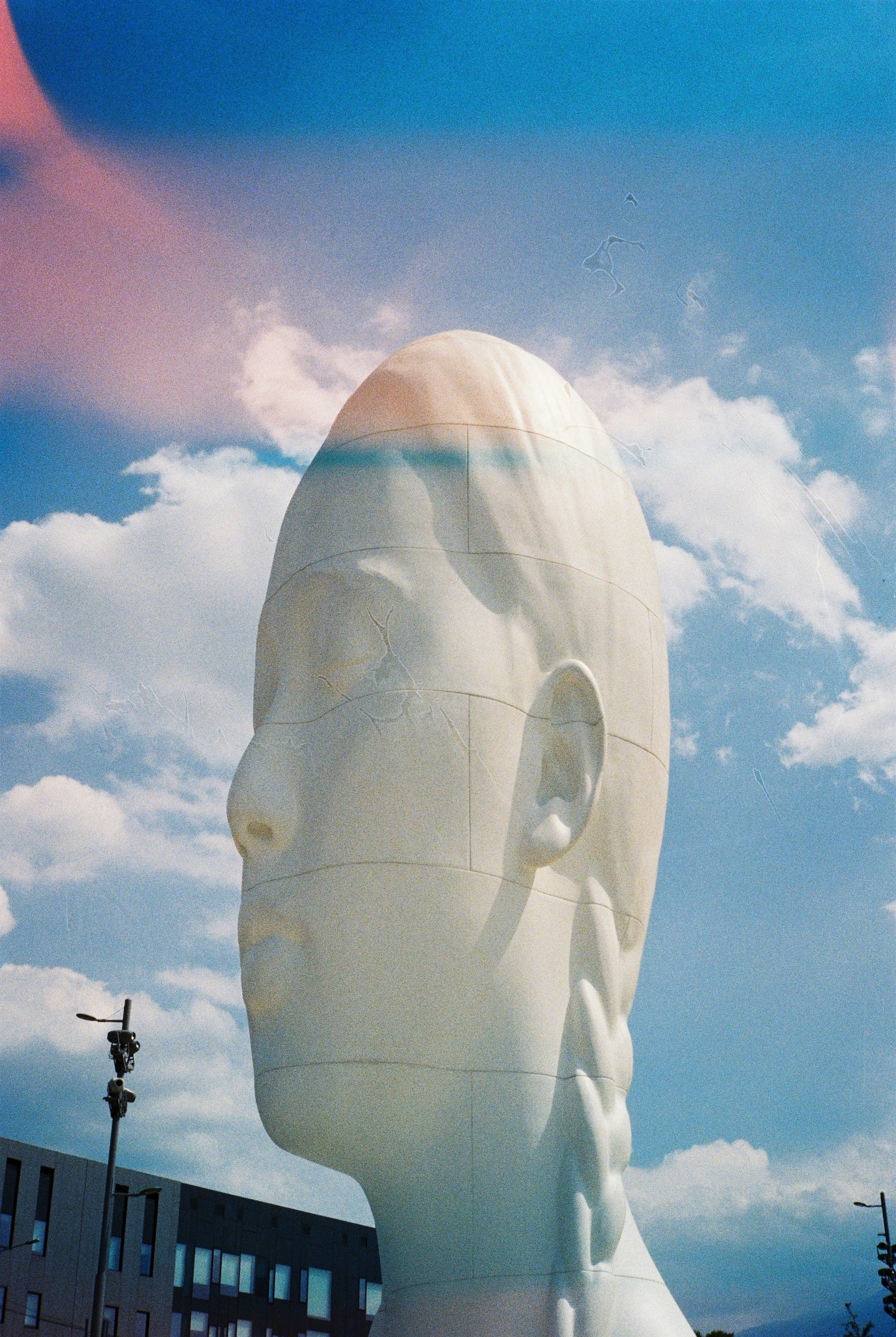 Giant white head sculpture against a cloudy blue sky
