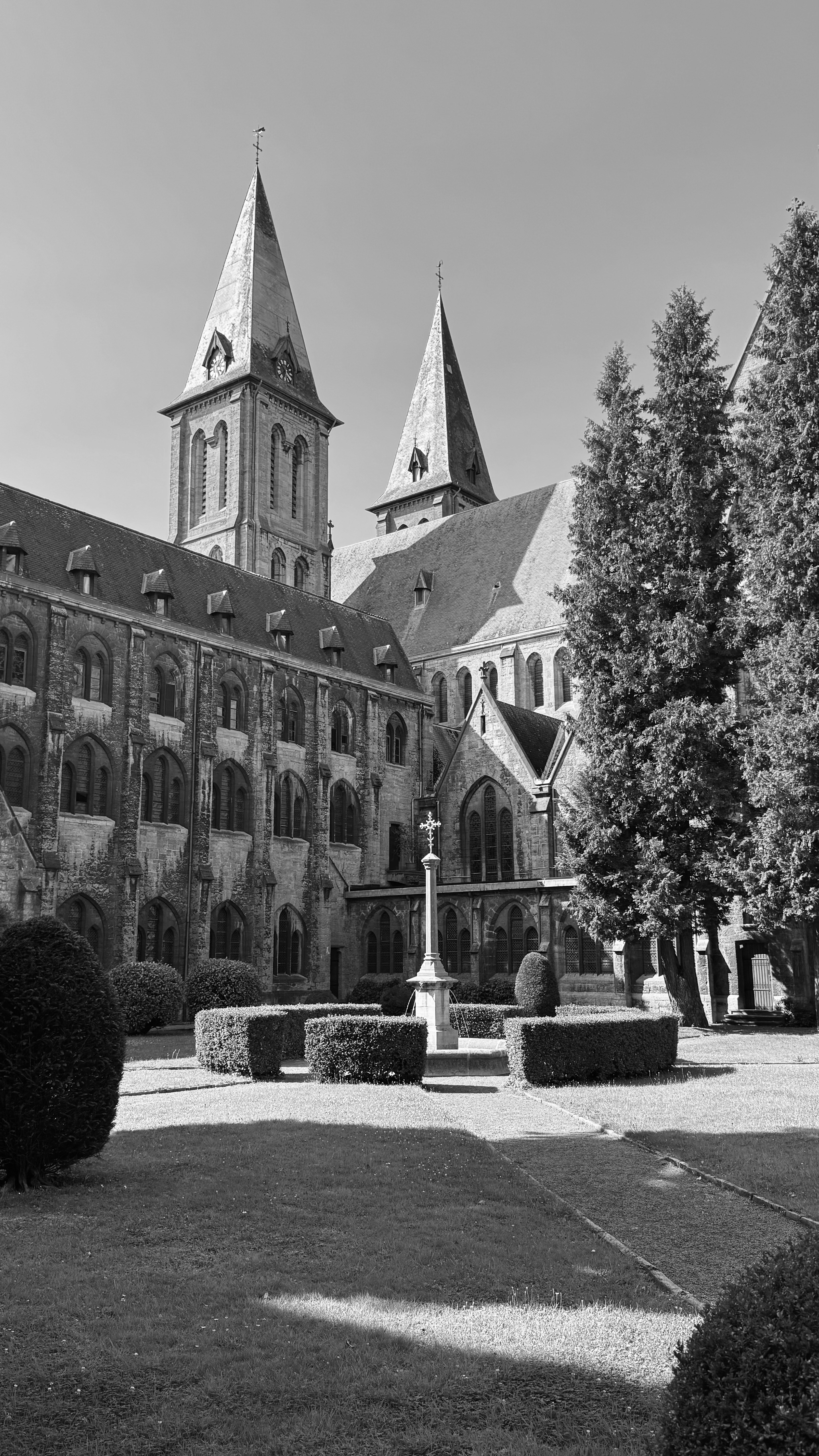 Historic monastery featuring intricate stonework and towering spires, surrounded by manicured gardens and hedges.