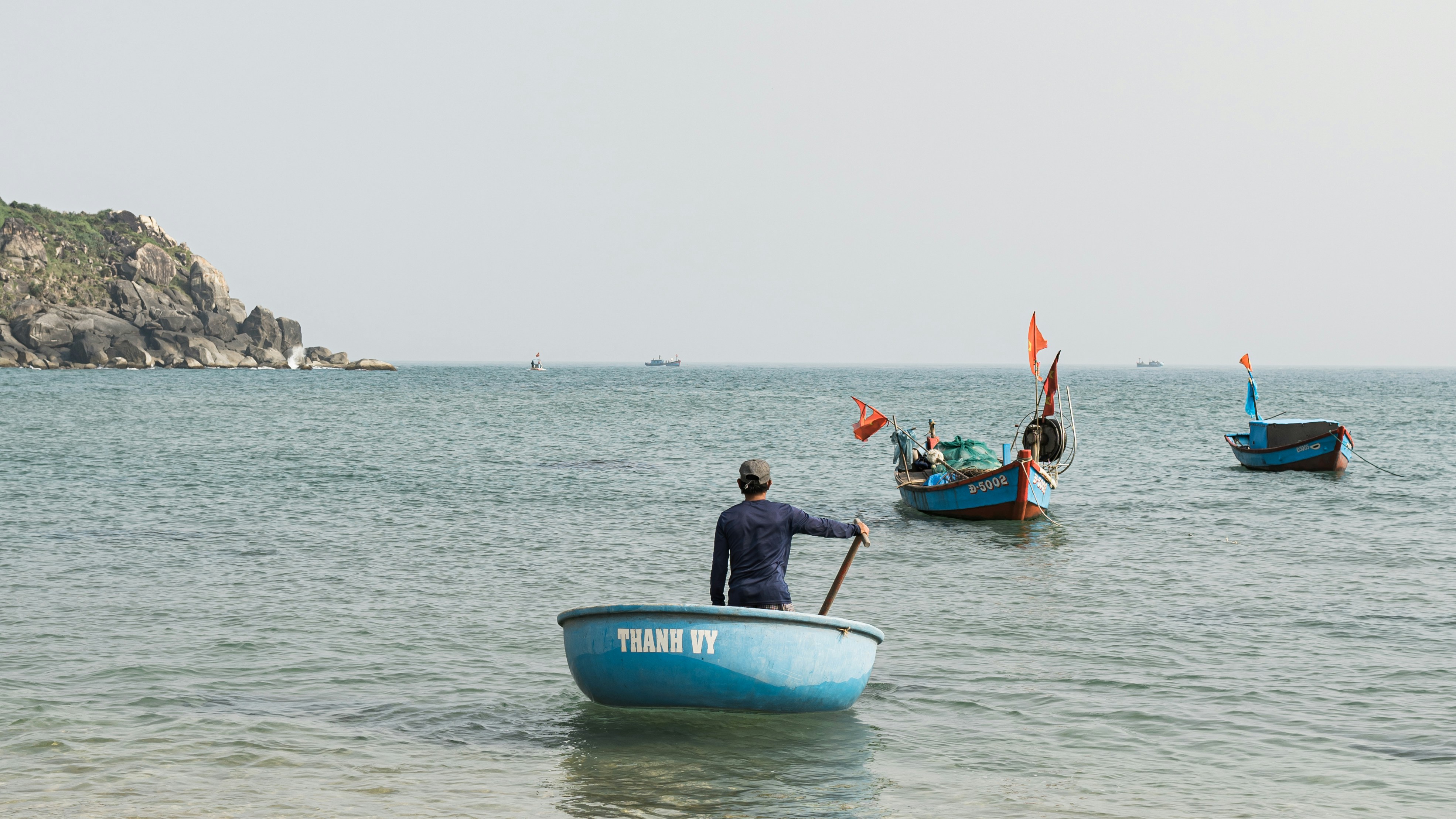 Fisherman rows a round boat towards other fishing boats.